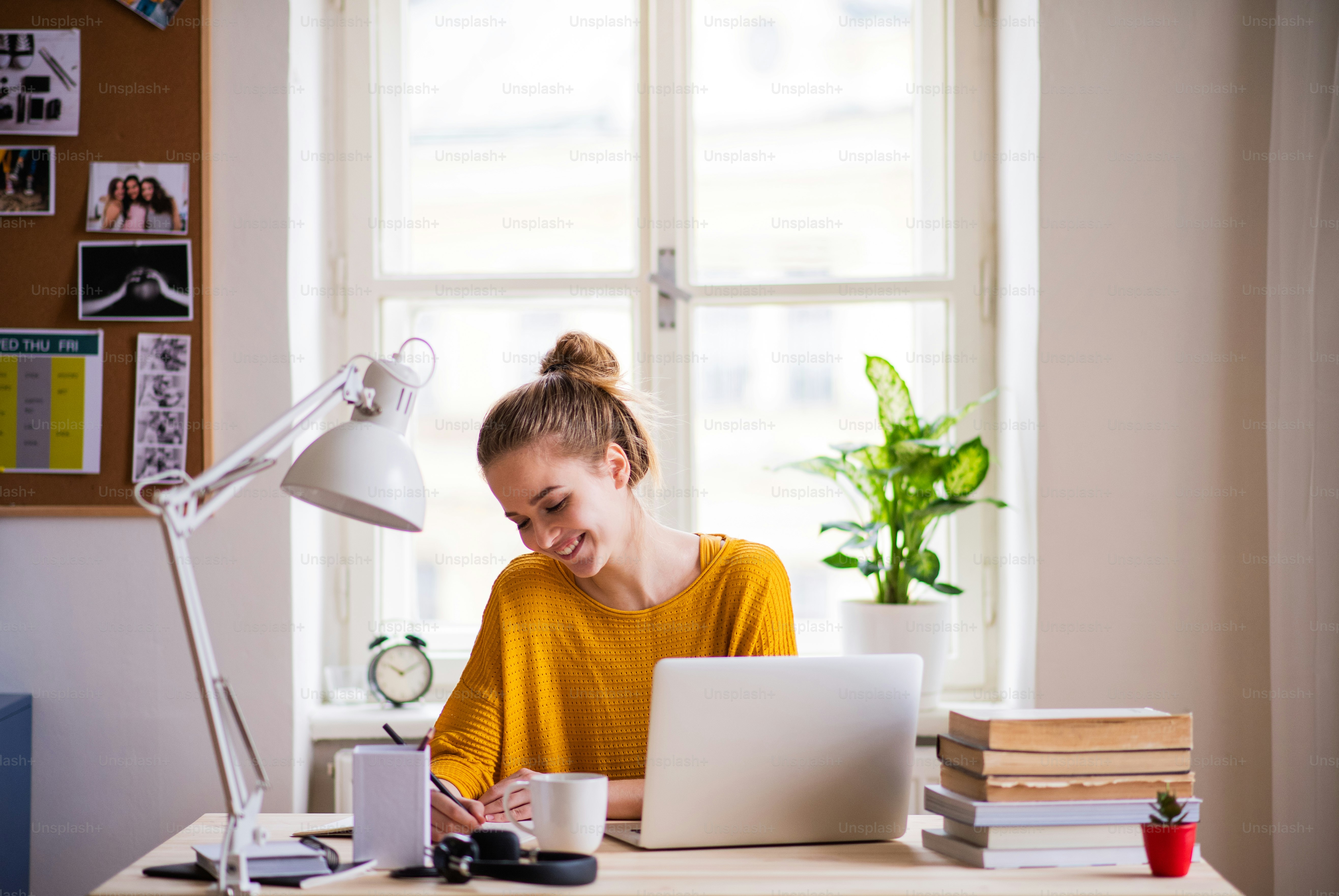 A young happy college female student sitting at the table at home ...
