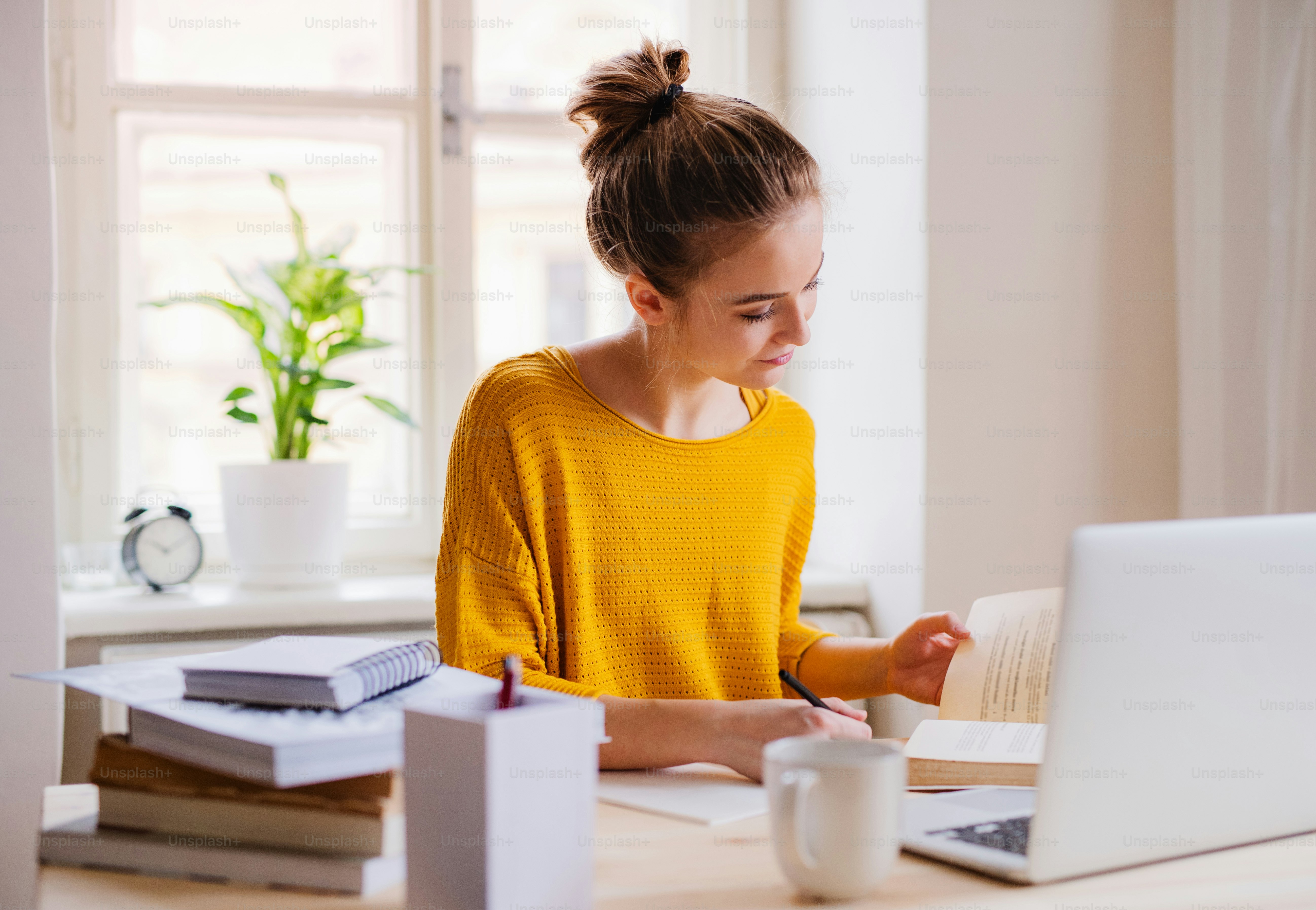 A young happy college female student sitting at the table at home ...