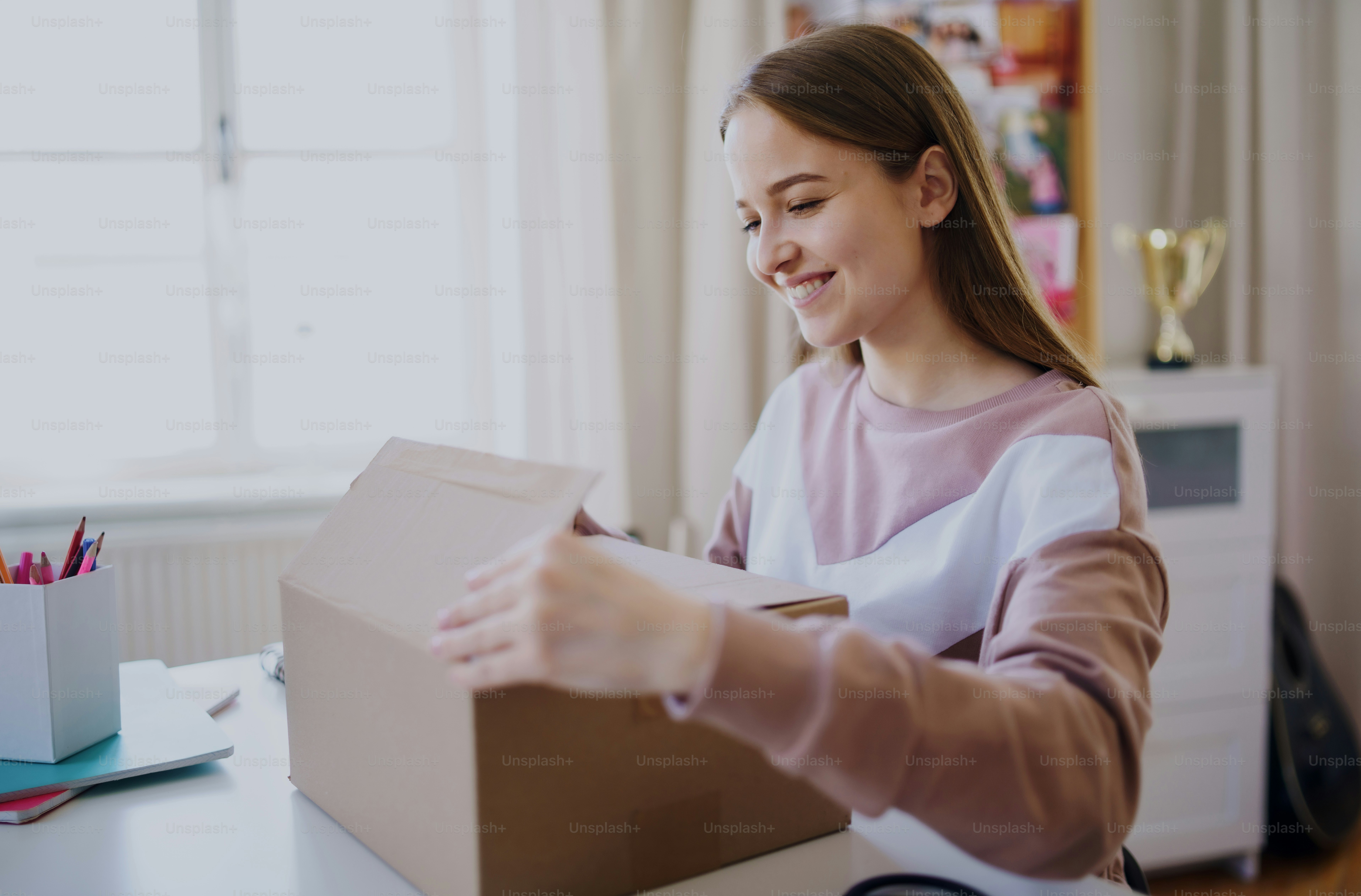 Side view of young female student at the table, opening parcel box ...