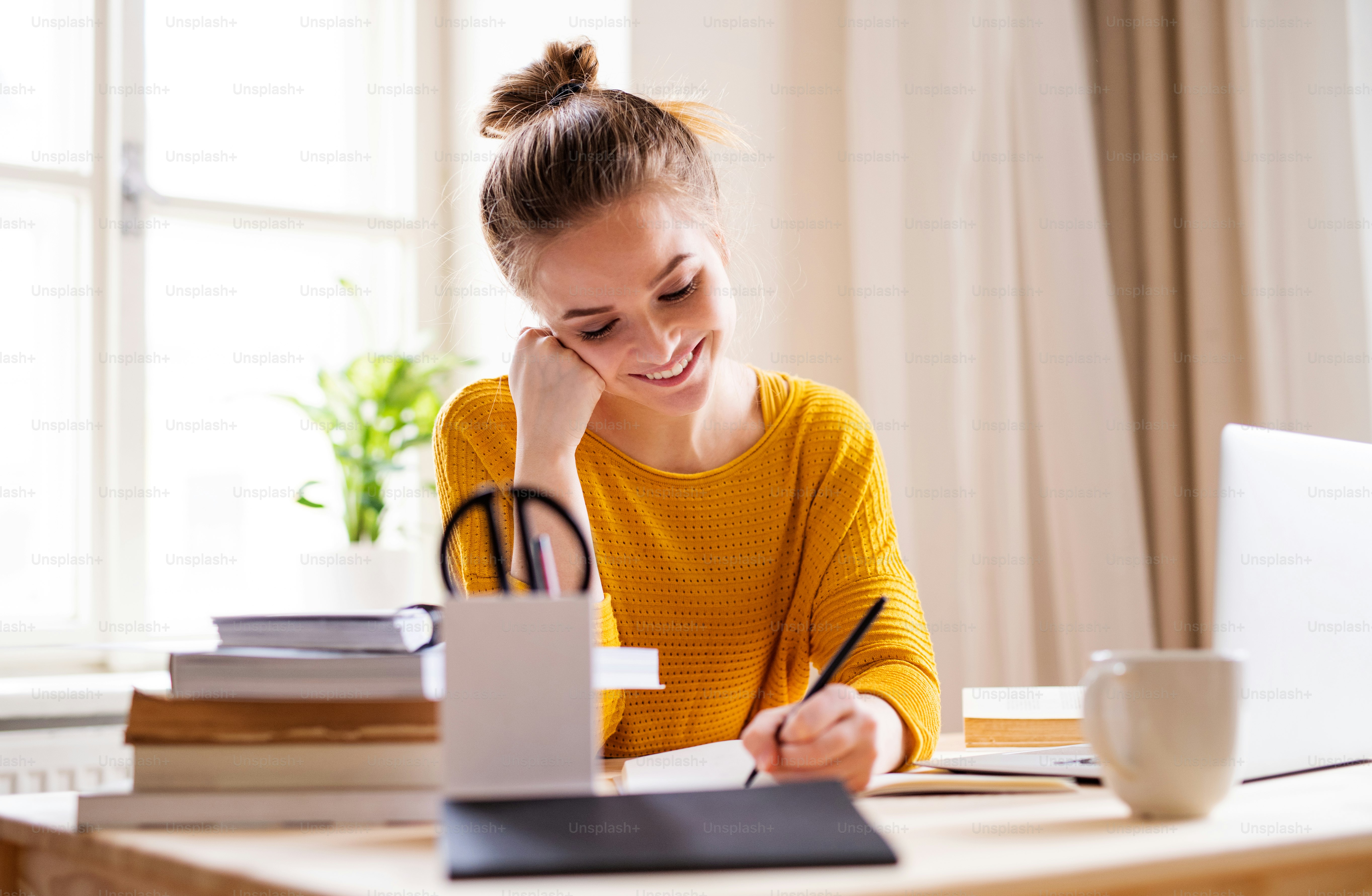 A young happy college female student sitting at the table at home ...