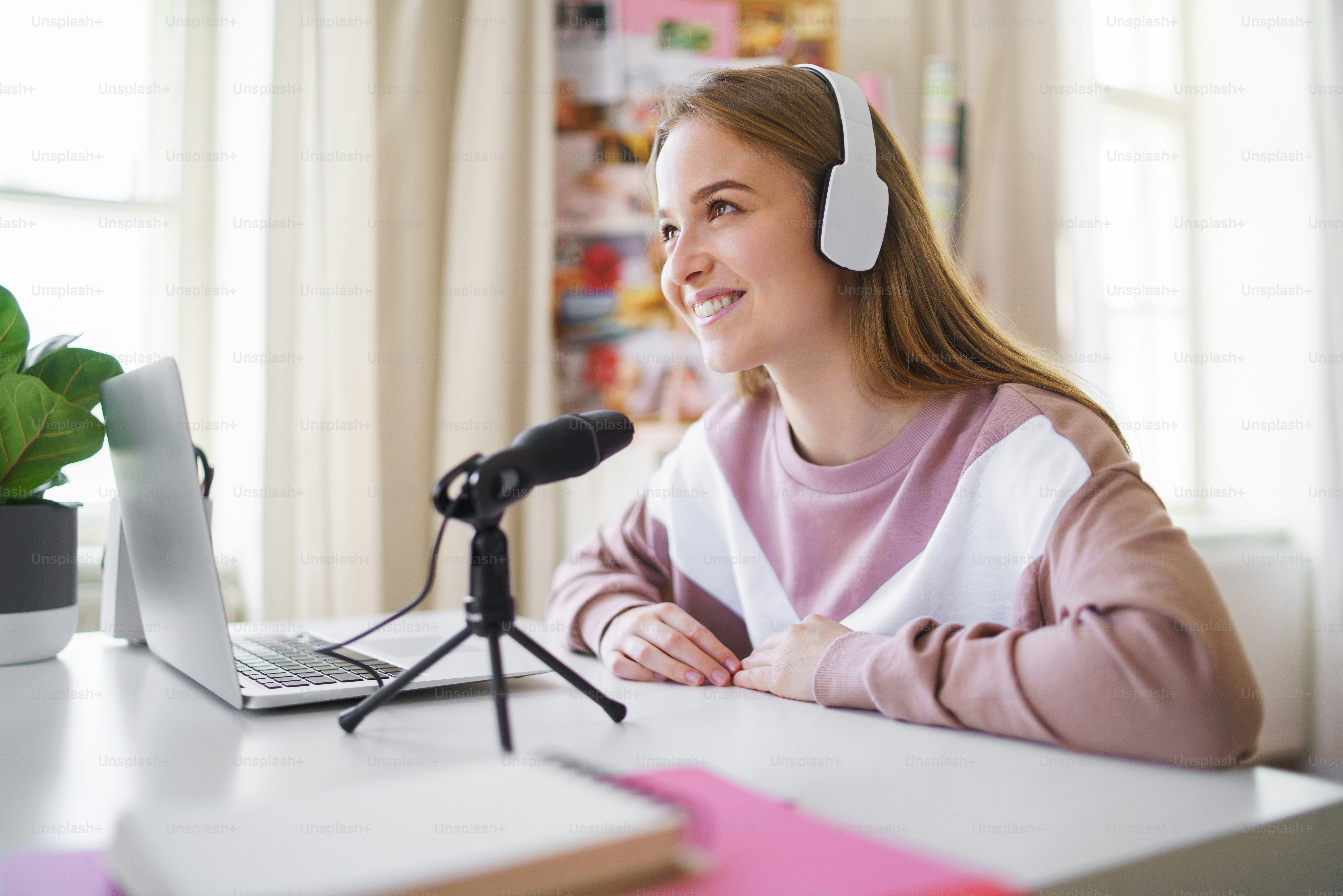 Young female student with laptop and microphone sitting at the table ...