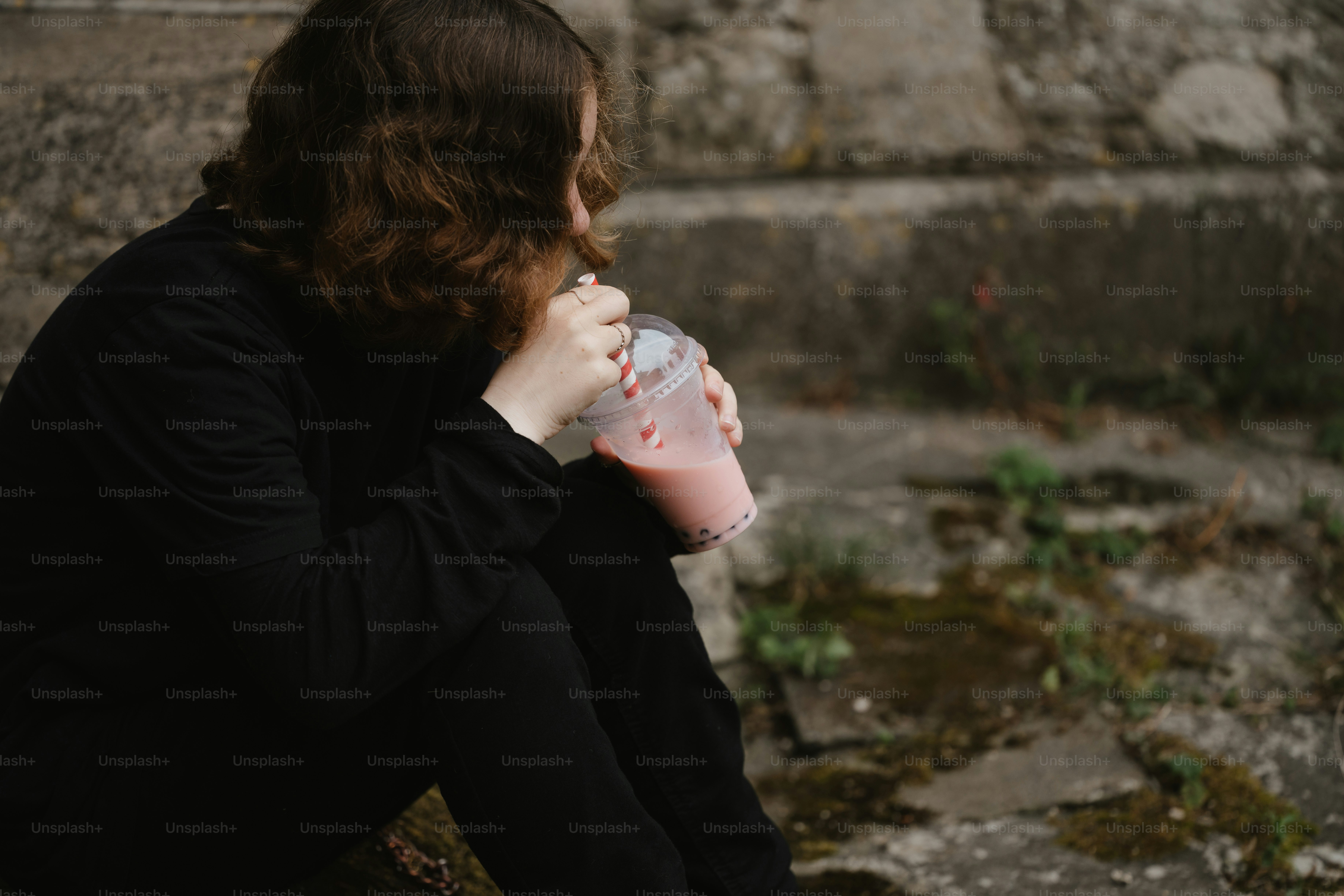 A woman sitting on the ground drinking from a pink cup photo – Bubble ...
