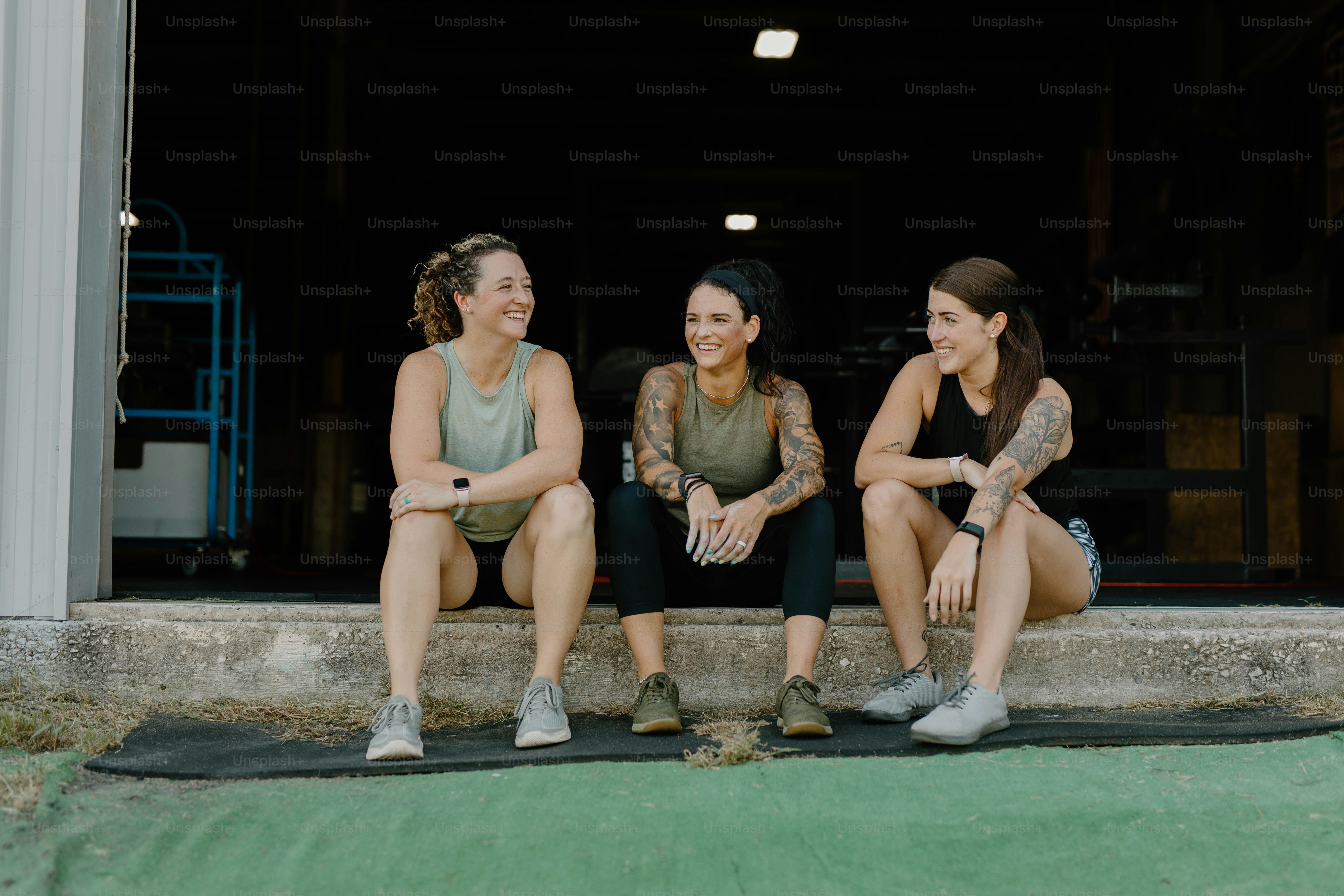Three women sitting on a ledge laughing photo – Female Image on Unsplash