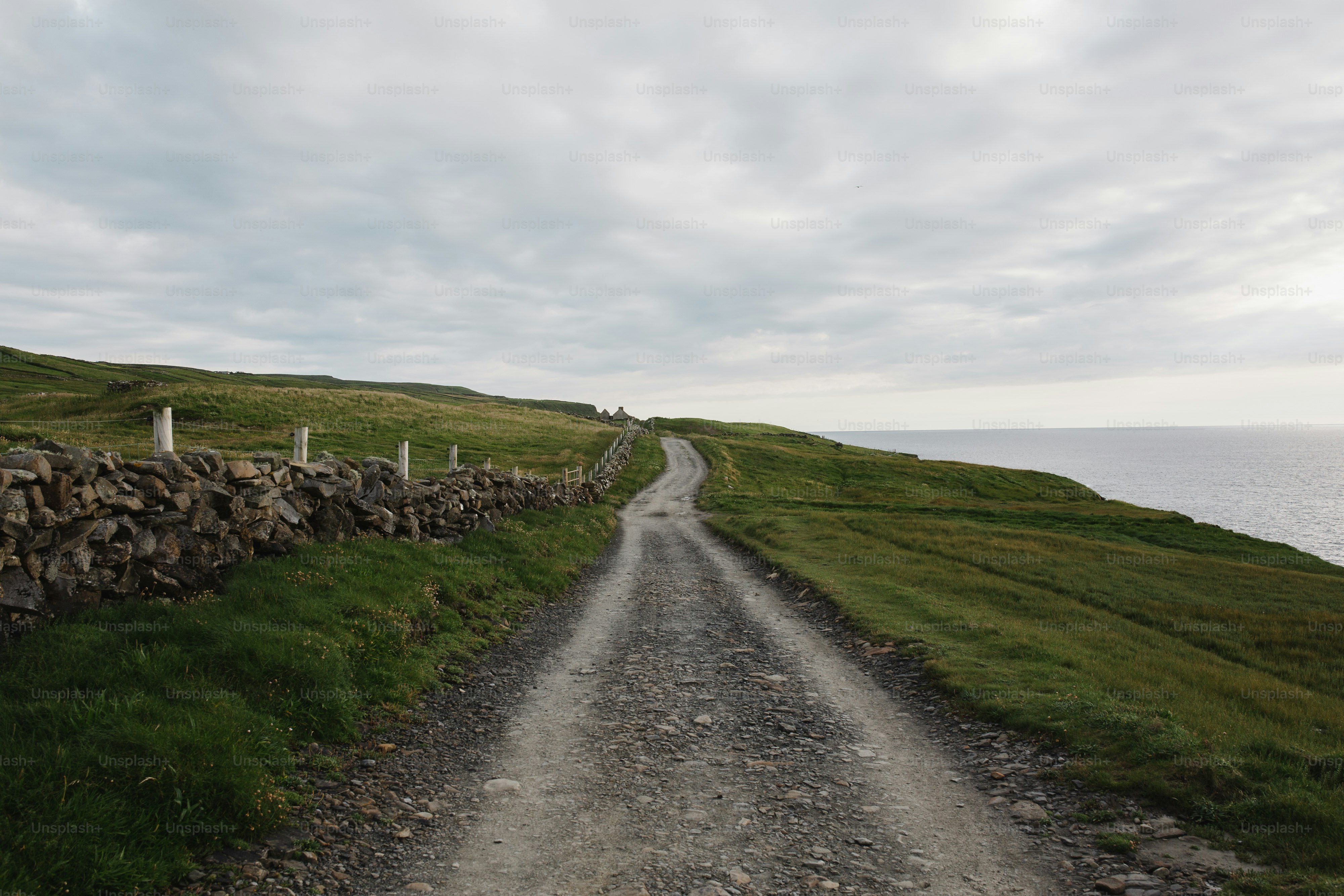 A gravel road with a stone wall next to the ocean photo – Gravel road ...