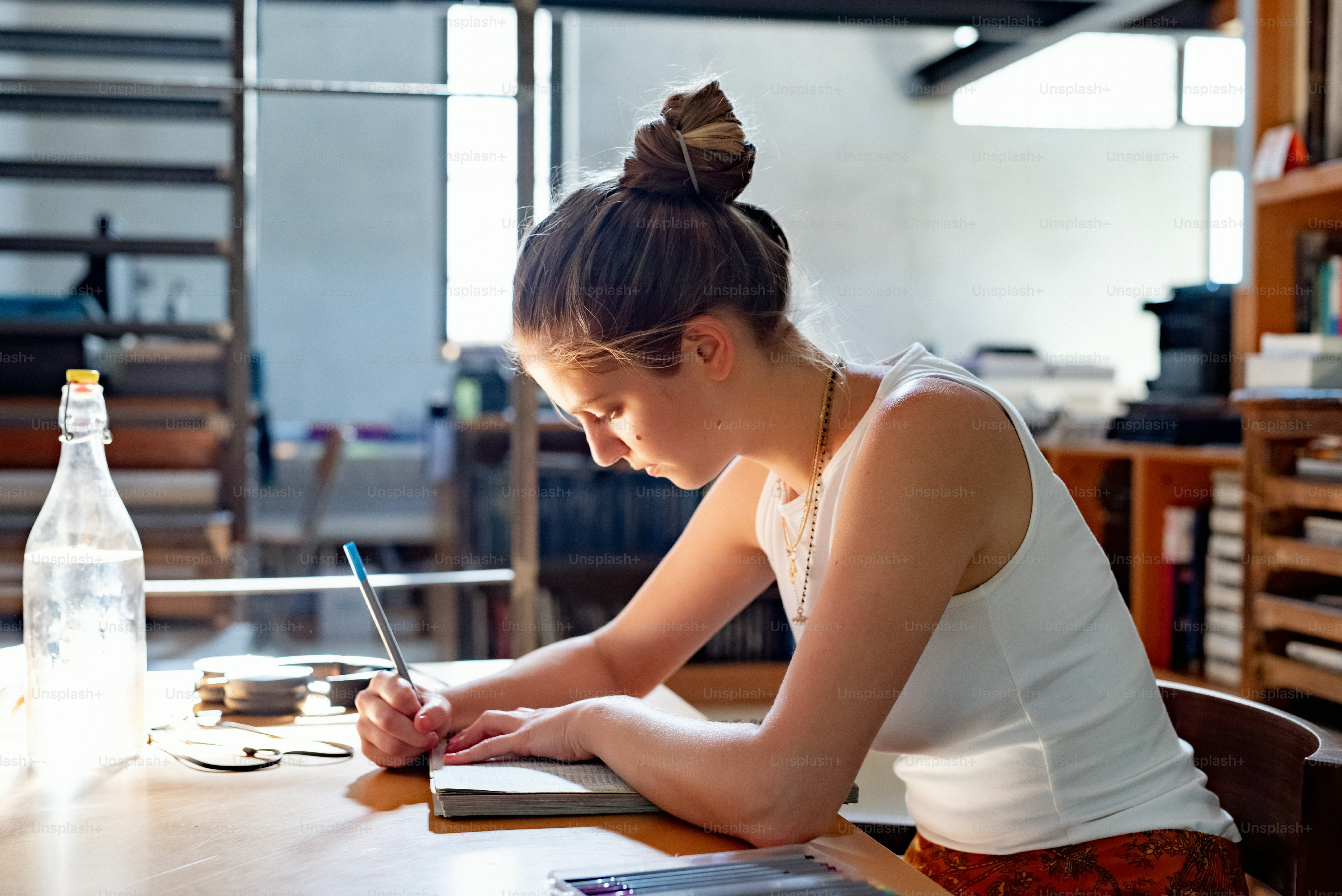 A woman sitting at a table writing on a book photo – Working women ...