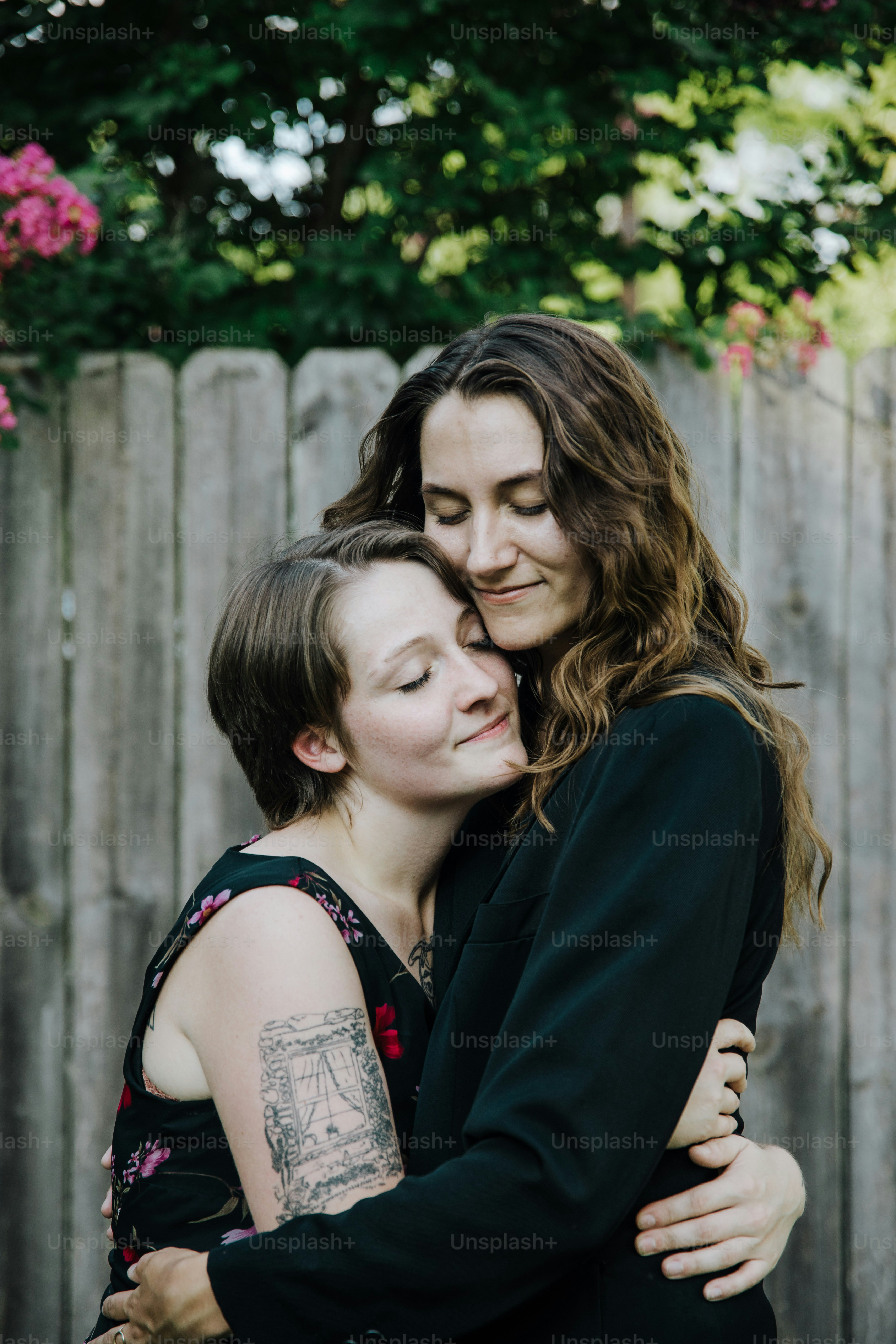 Two women hugging each other in front of a fence photo – Cuddle Image ...