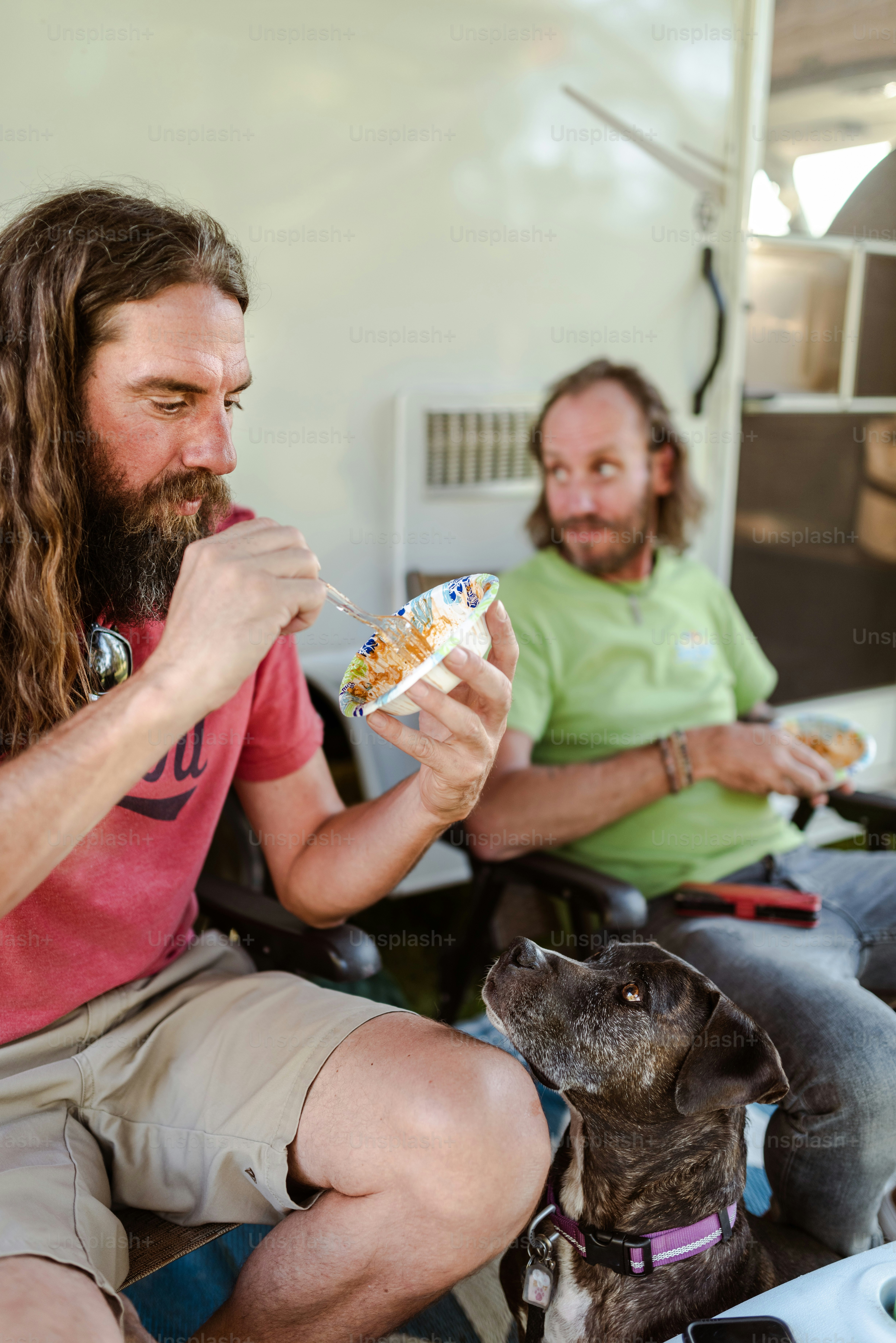 A man with long hair and a beard eating food next to a dog photo – Man ...