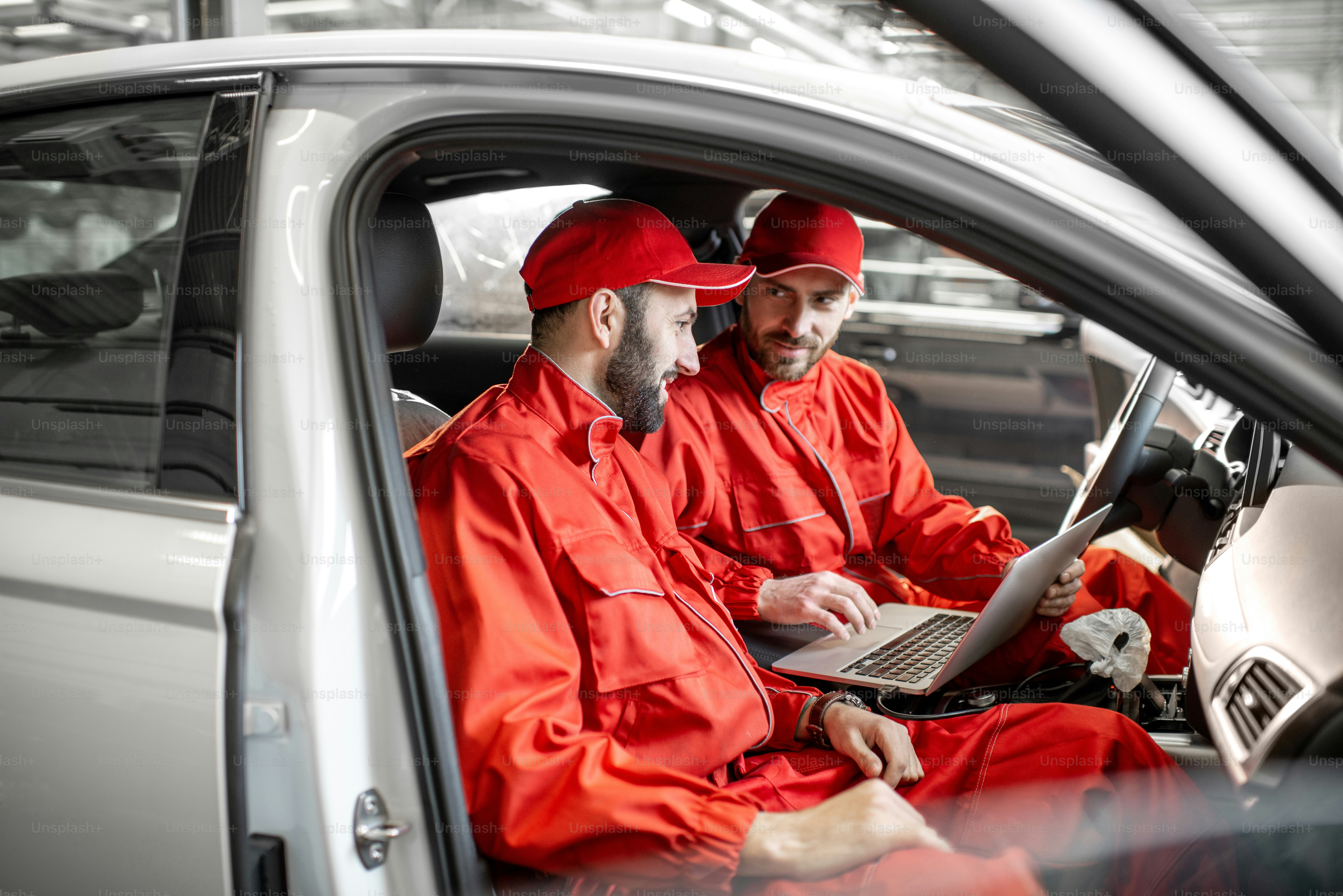 Two male auto mechanics in red uniform diagnosing car with computer ...