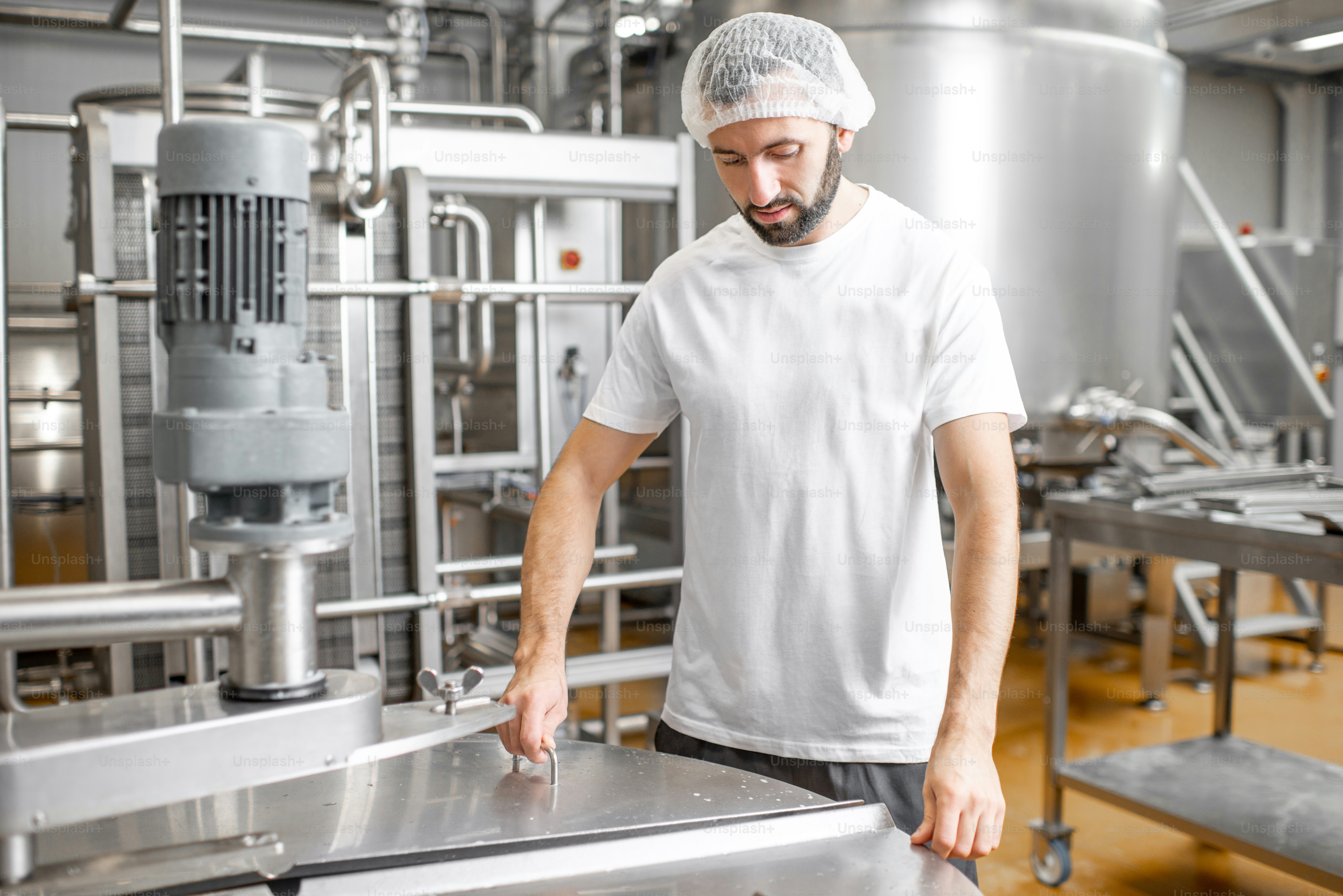 Portrait of a handsome worker in uniform near the stainless tank full ...