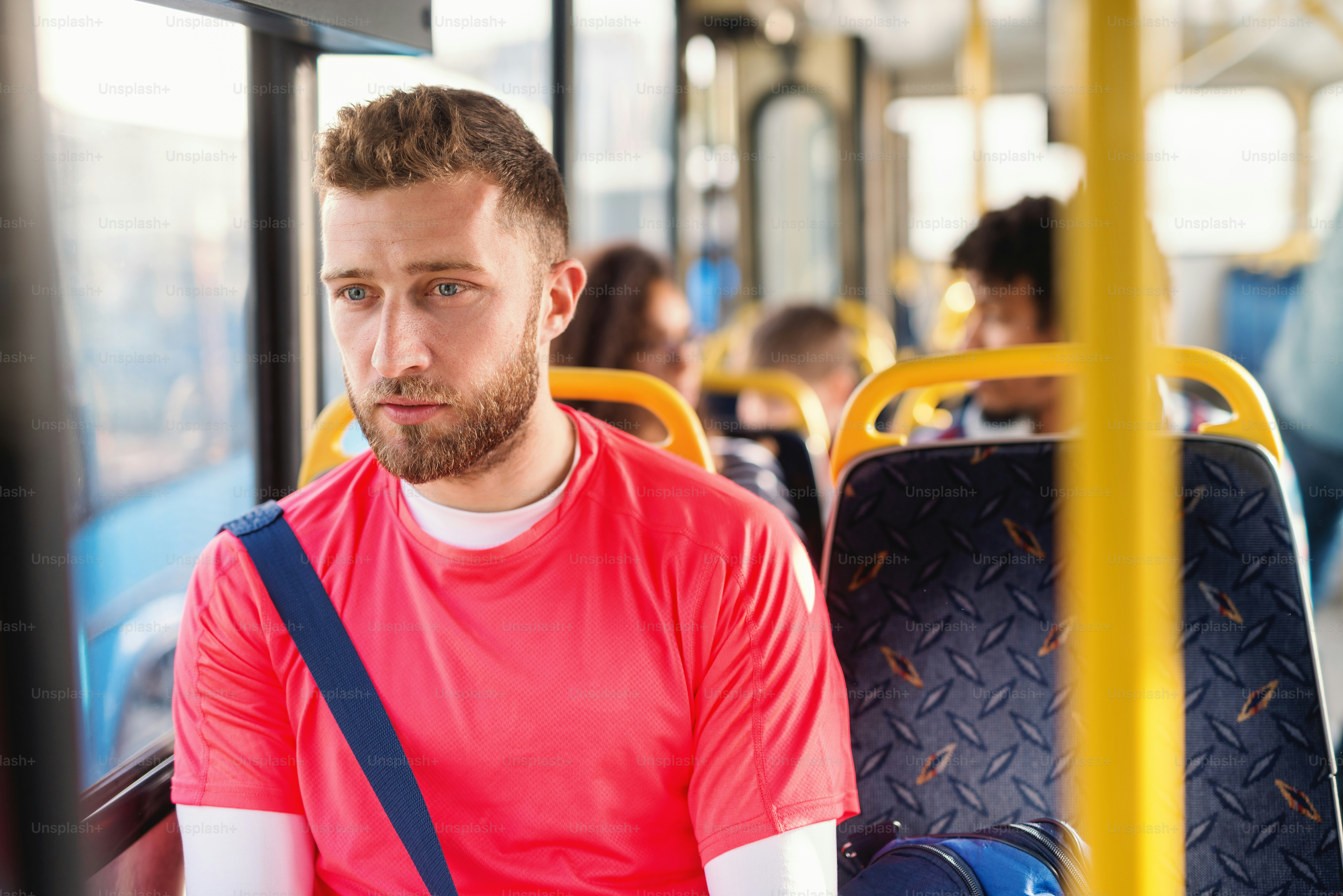 Young blonde sporty man with serious face sitting in the city bus ...