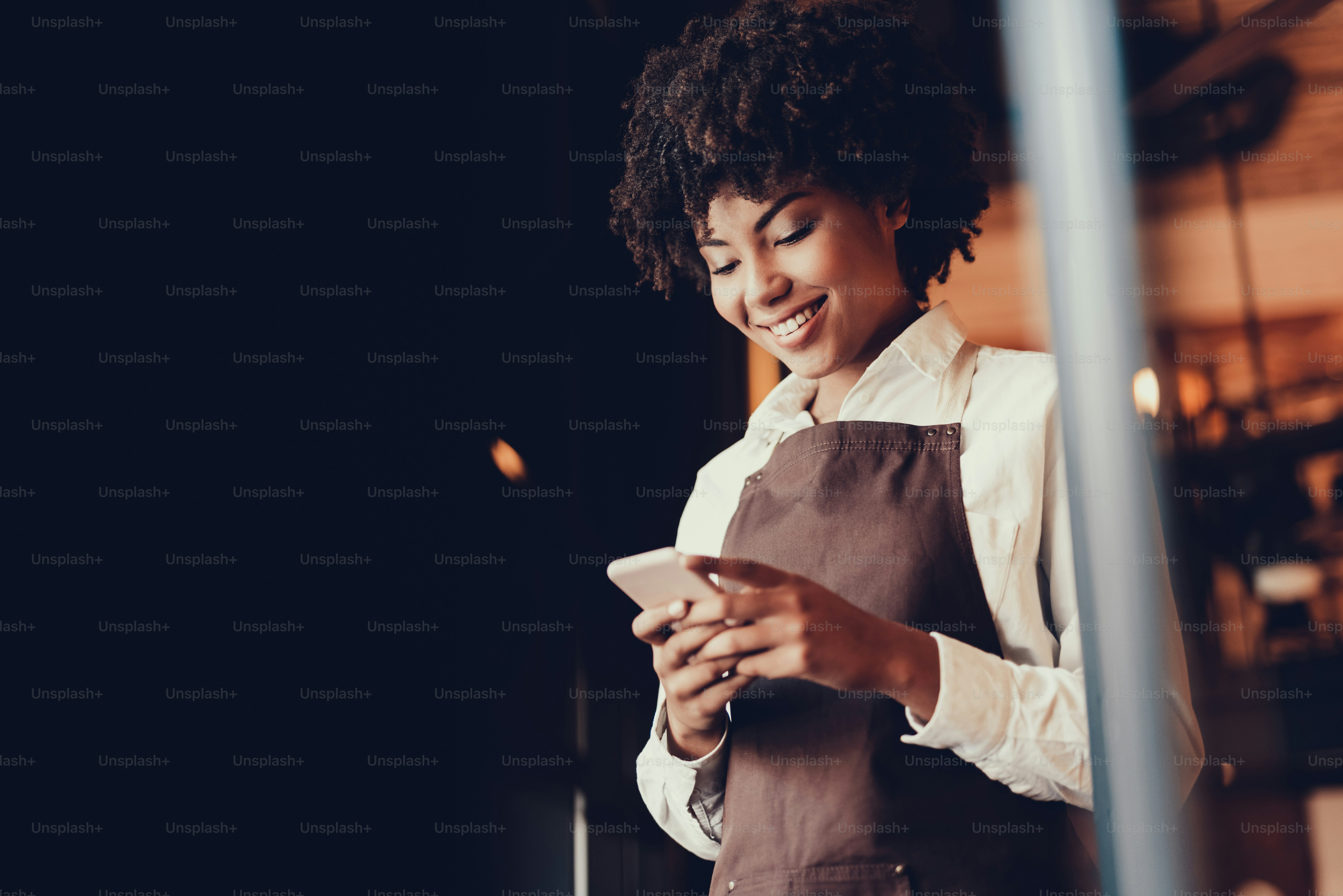 Cheerful lady waitress having break from work. She holding mobile phone ...