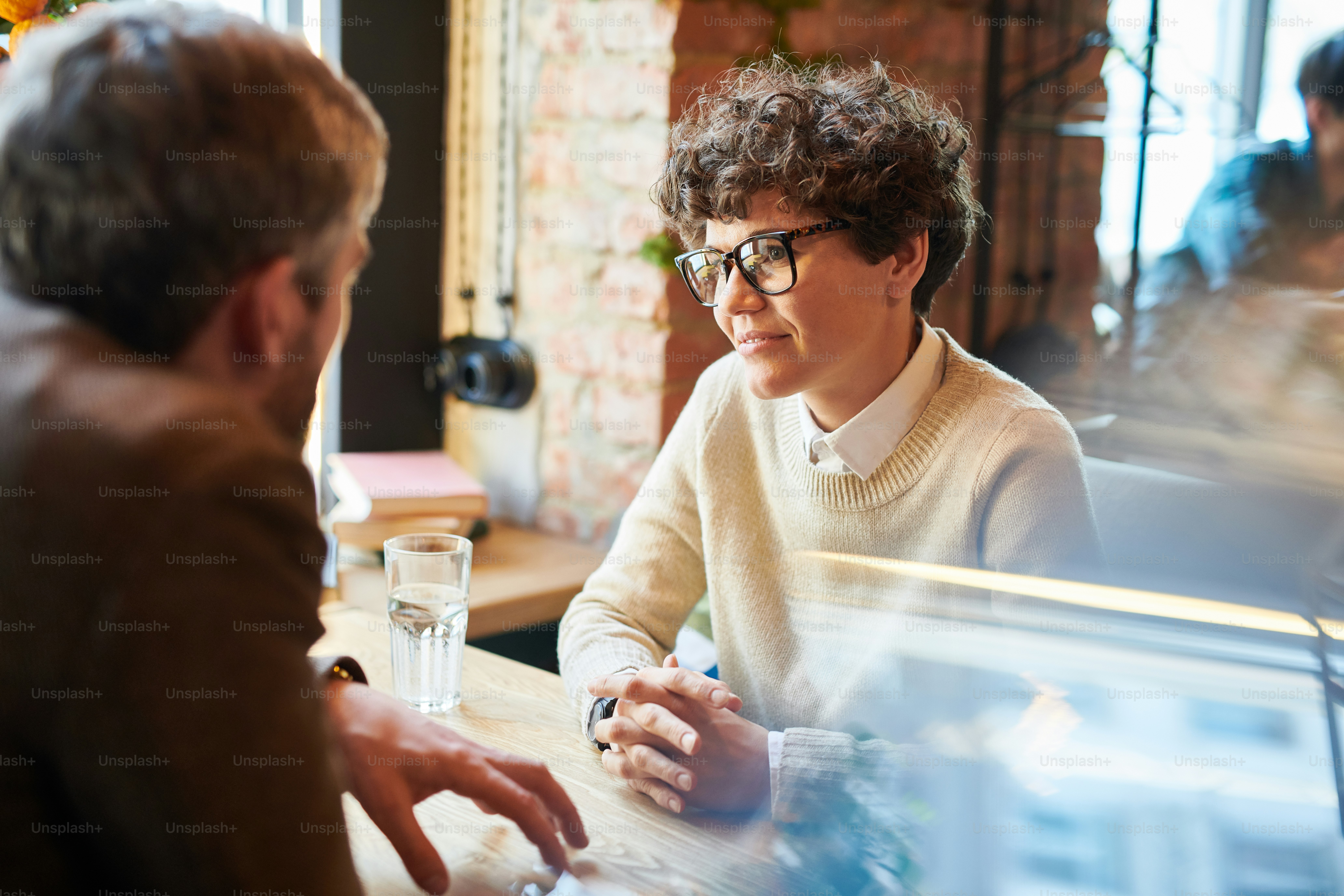 Pretty young businesswoman listening to her colleague or client ...