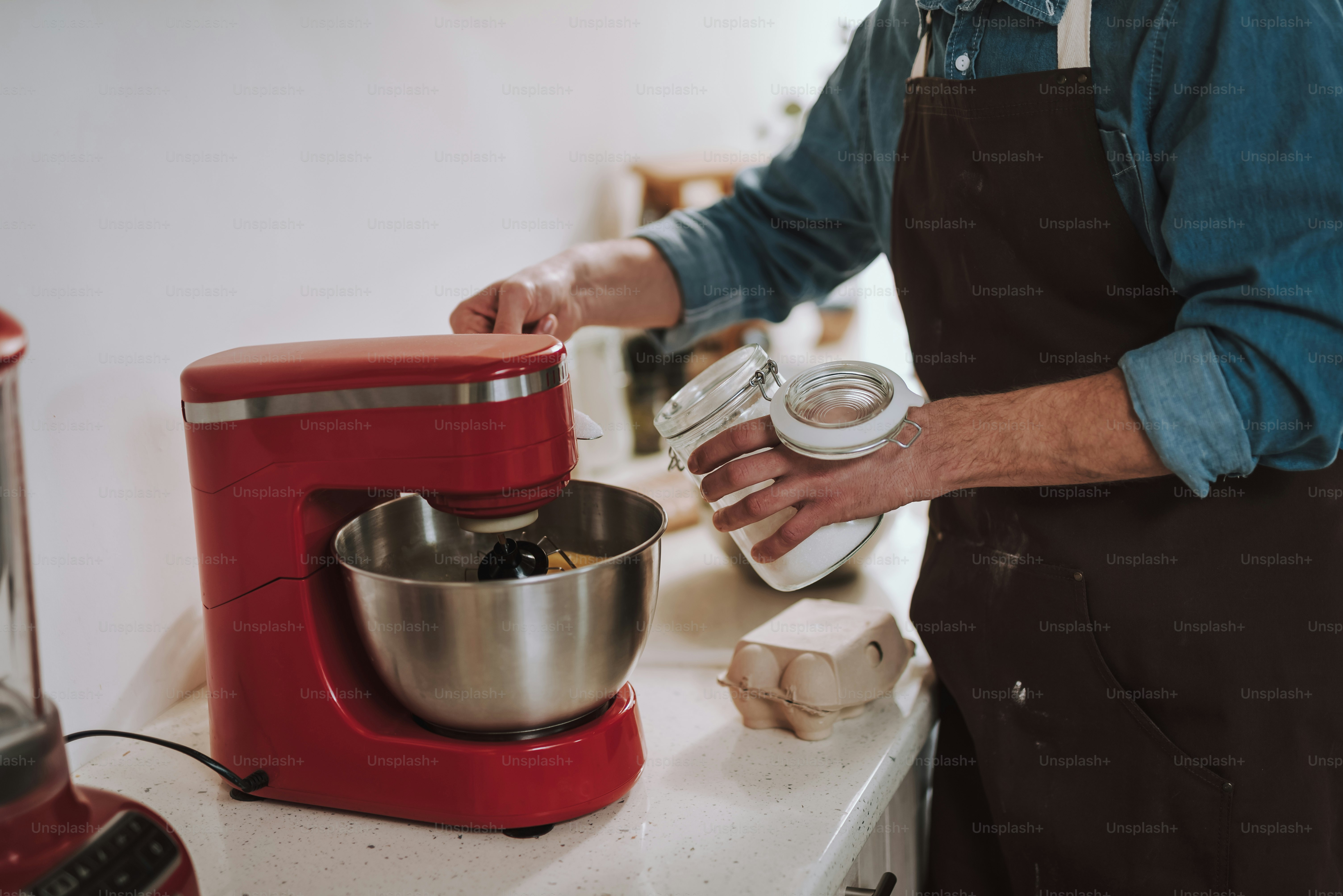 Man cooking in the kitchen and putting sugar from the jar into the bowl ...