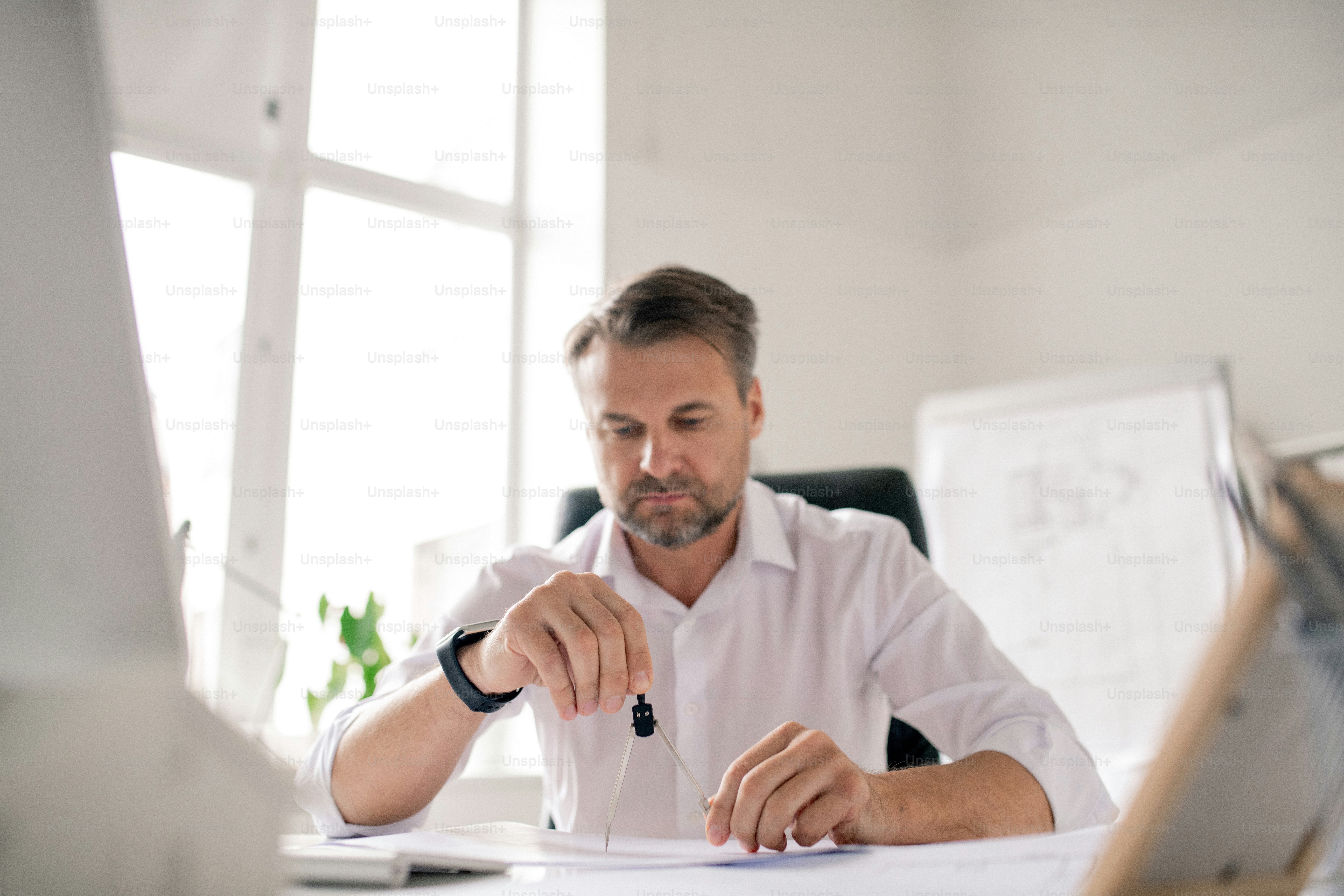 Casual mature engineer using dividers while drawing sketch of new ...