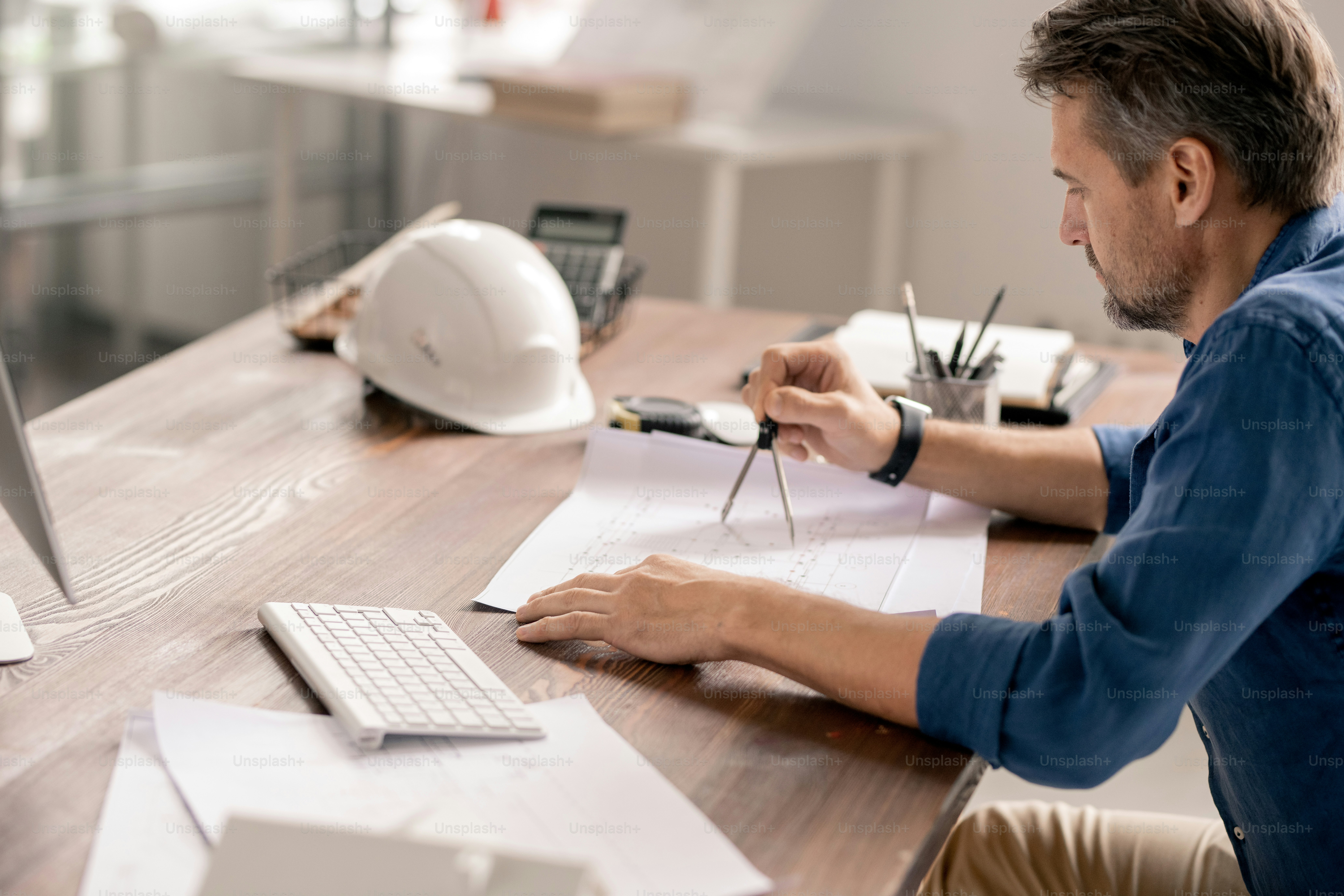 Casual mature engineer using dividers while drawing sketch of new ...