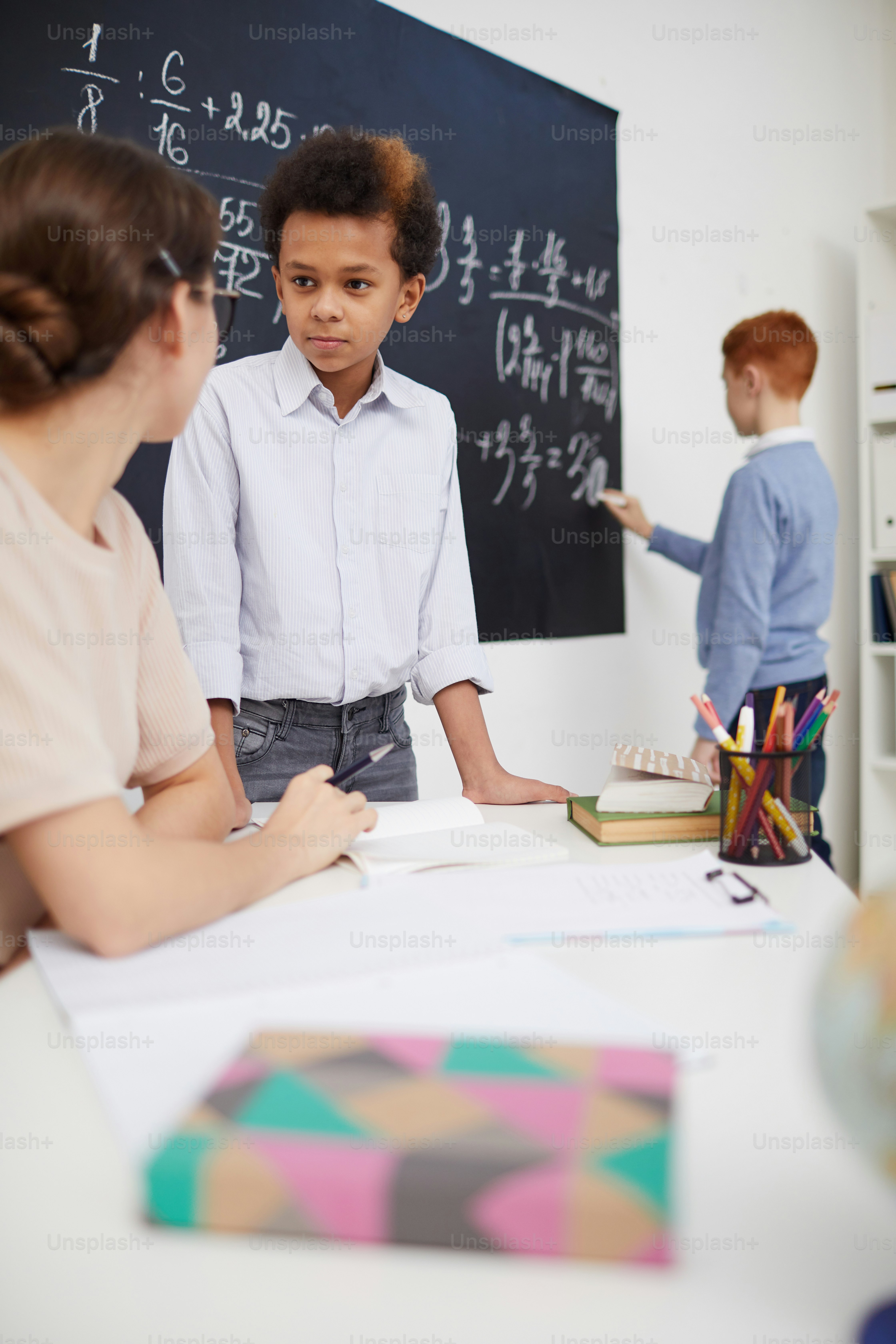 Young teacher checking the knowledge of schoolboy during maths lesson ...
