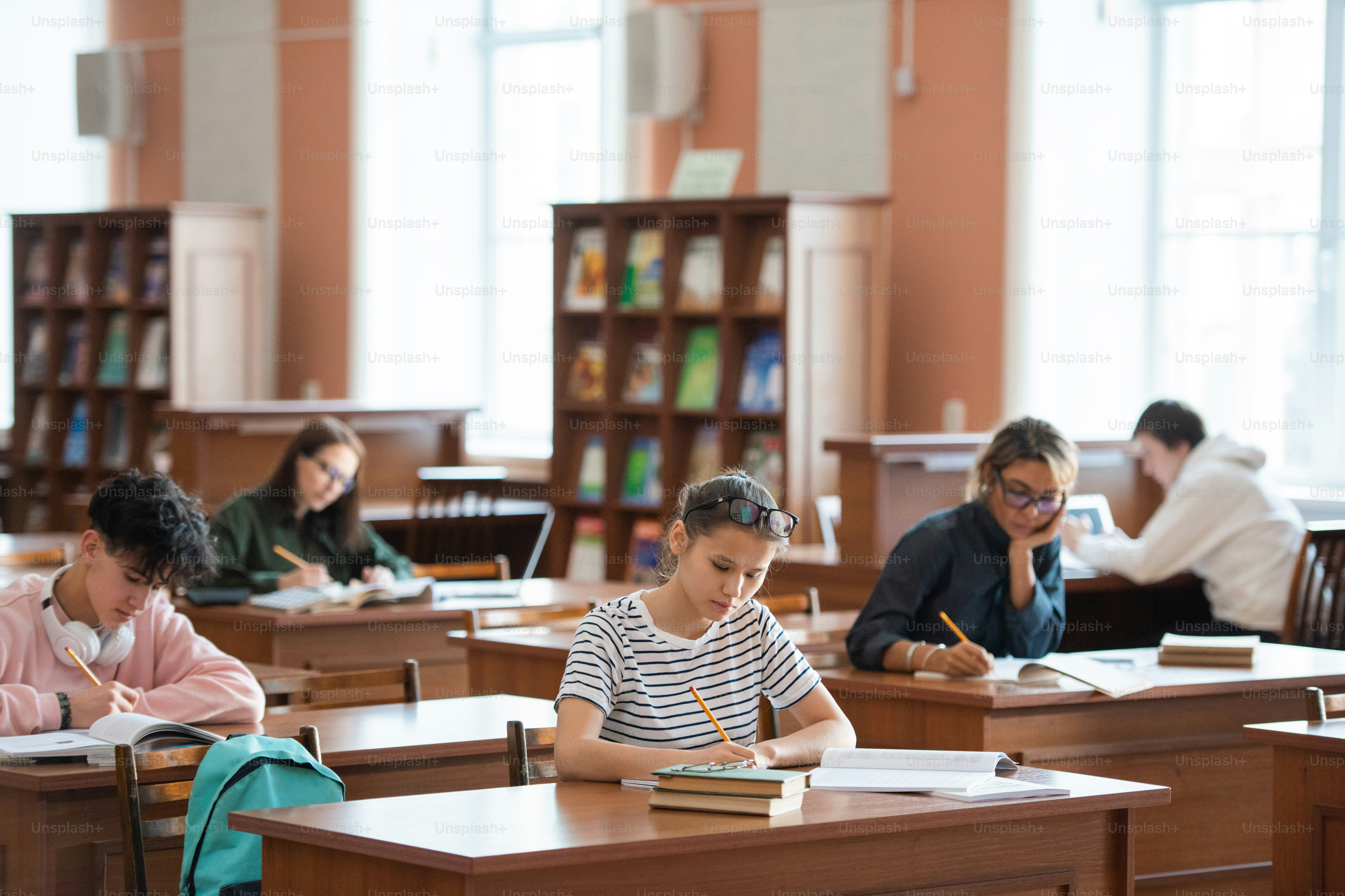 Group of contemporary college learners sitting by desks in library and ...