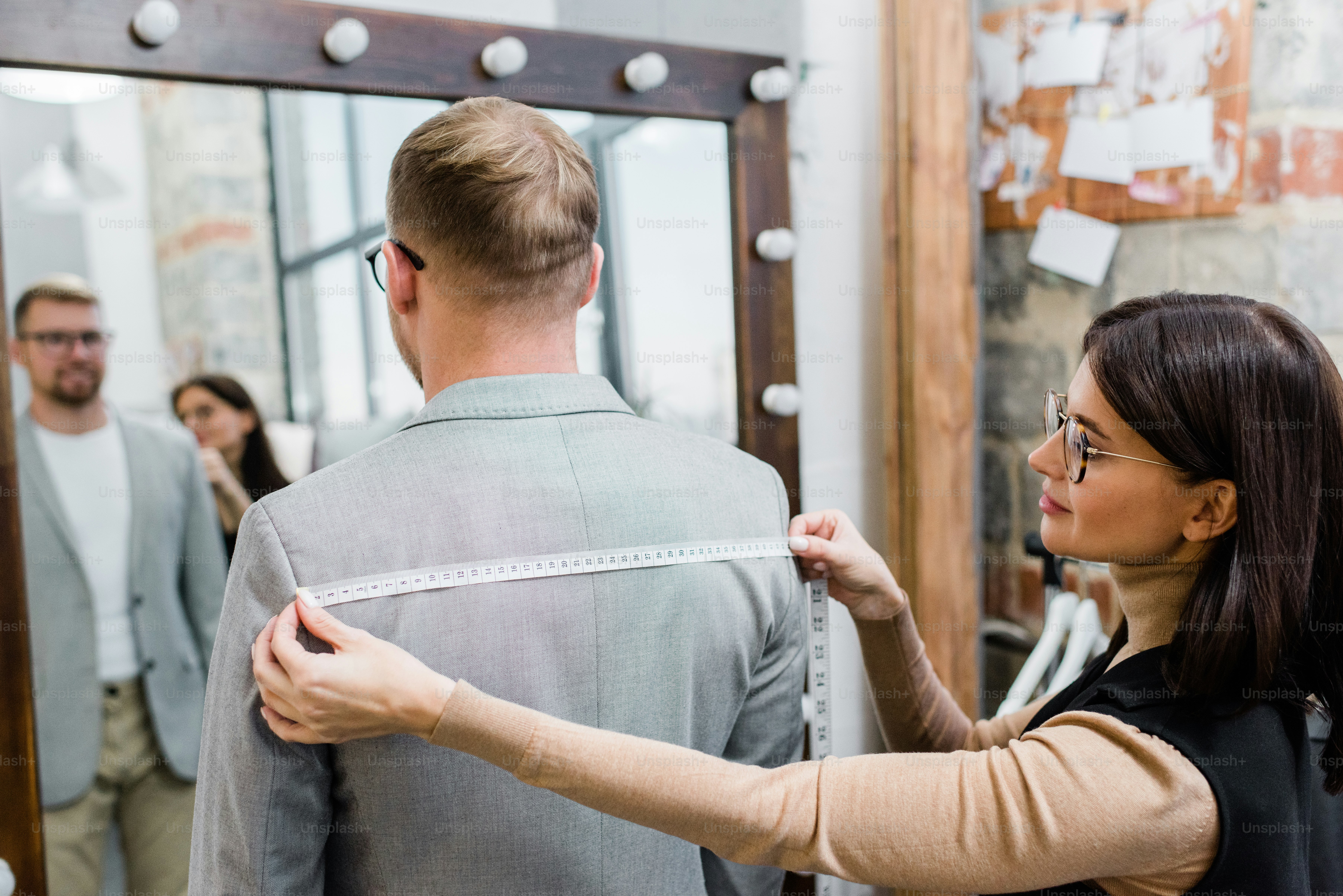 Rear view of female tailor measuring width of clients shoulders in own ...