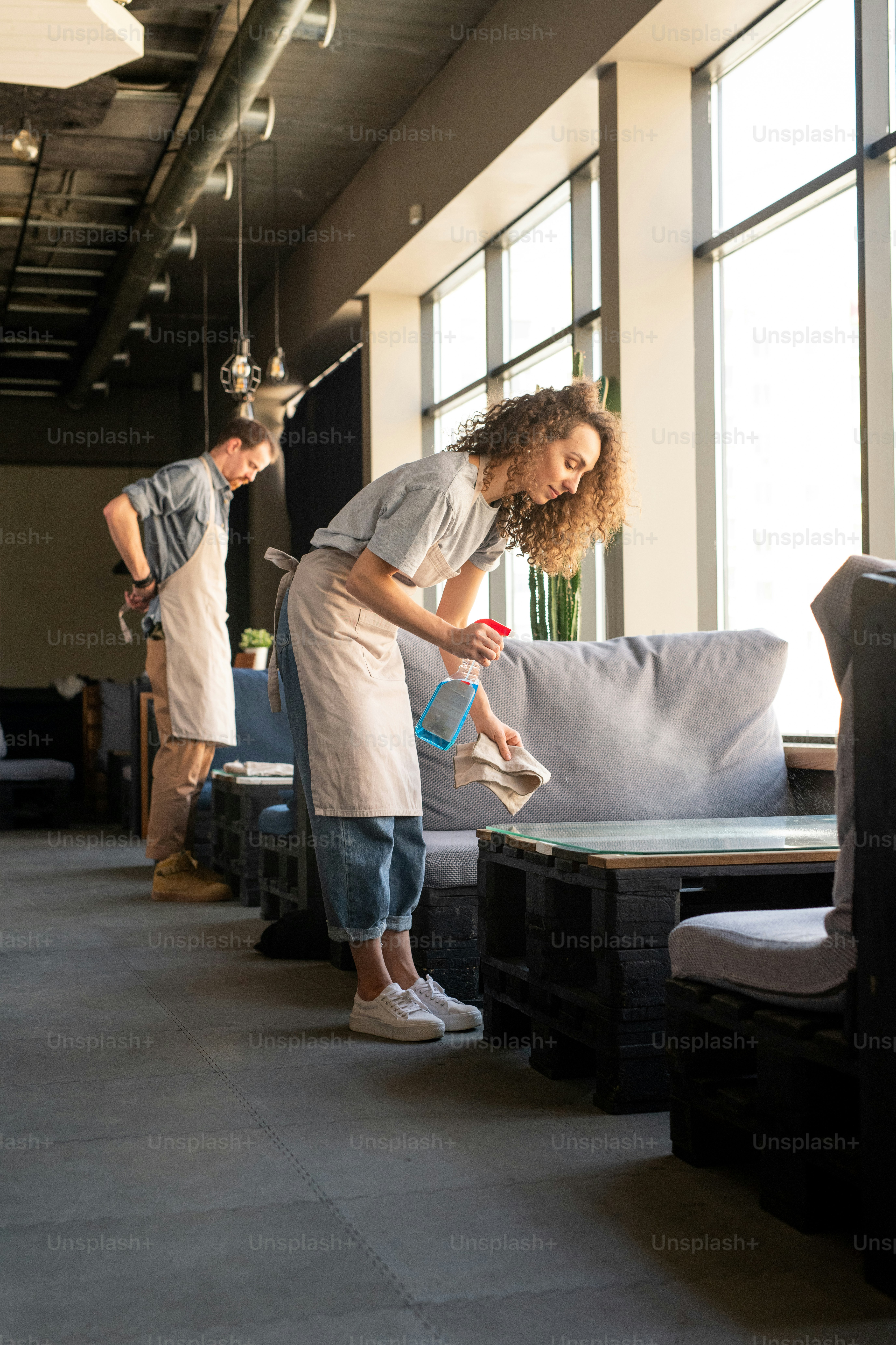 Pretty young waitress in casualwear and apron bending over one of ...