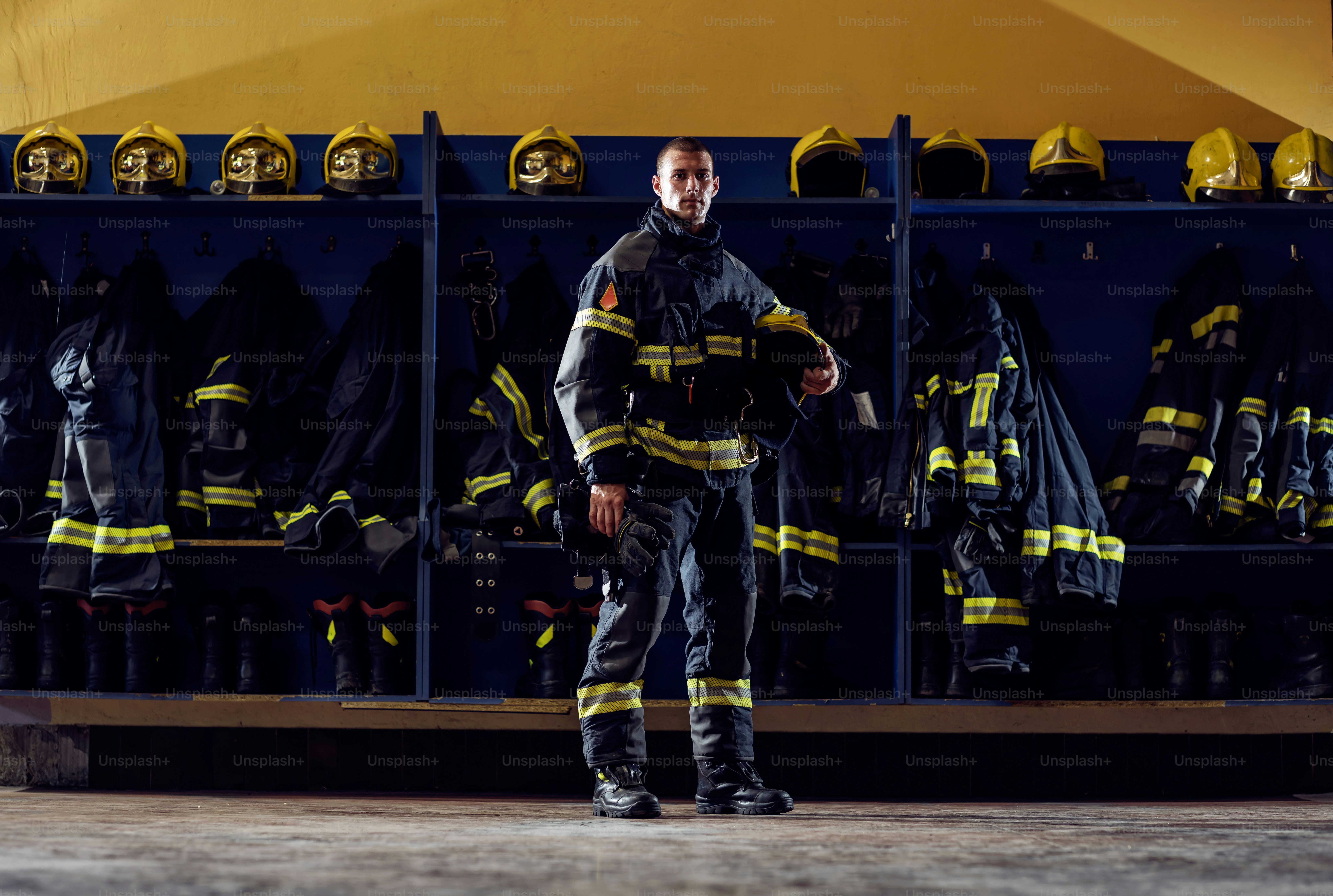 Brave young firefighter standing in fire station in protective uniform ...