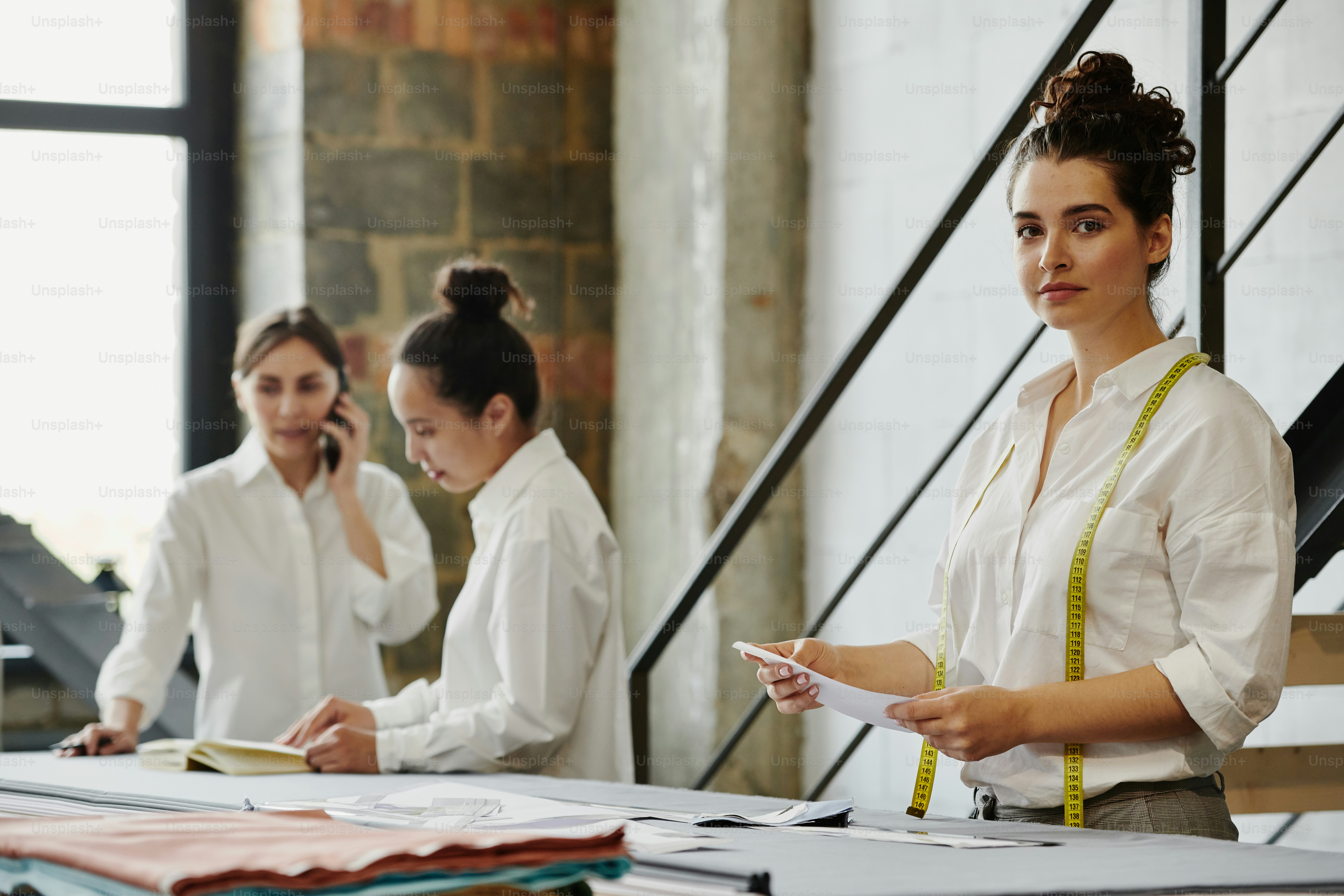 Young serious seamstress with measuring tape and paper patterns looking ...