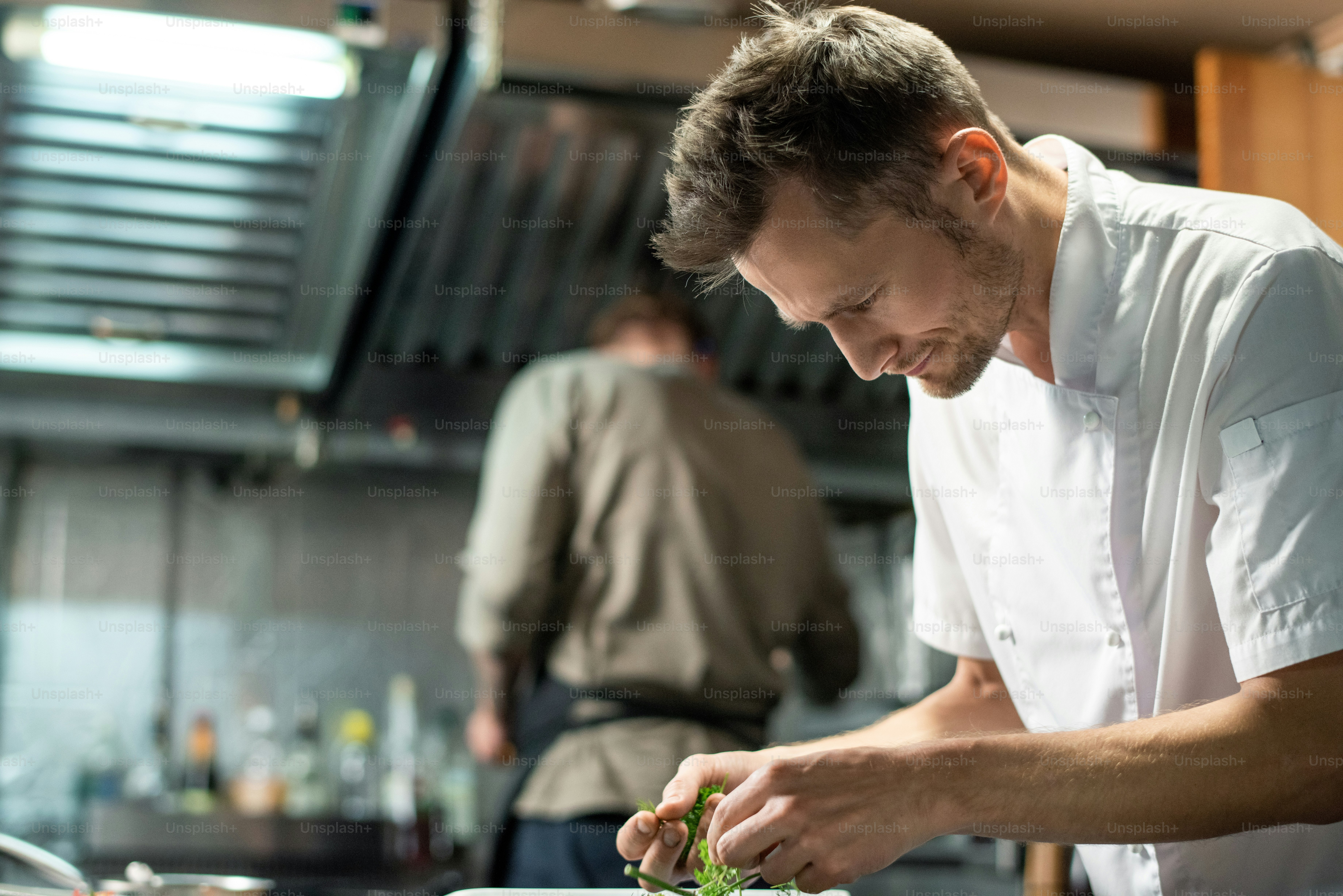 Contemporary young professional male chef bending over kitchen table ...
