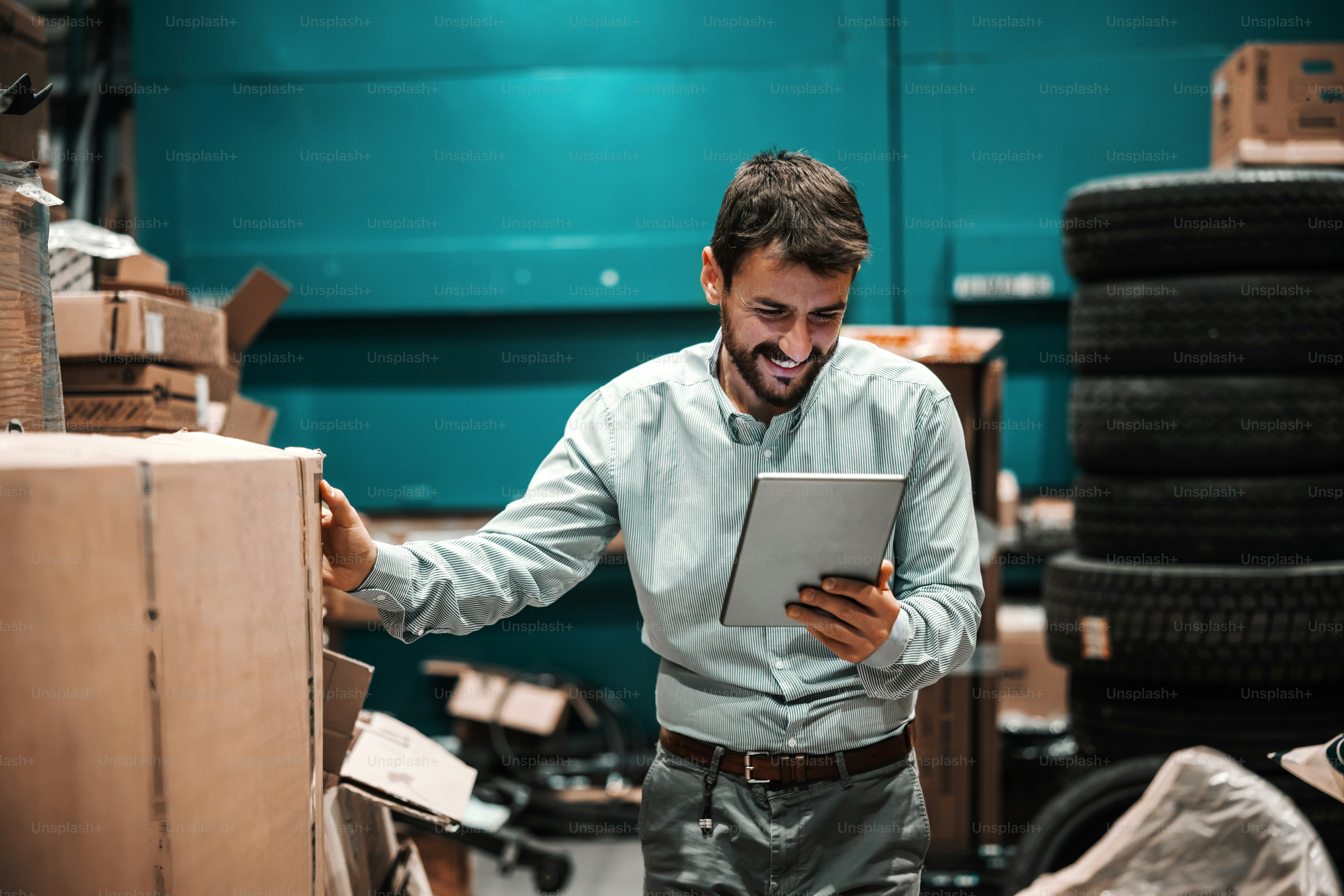 Smiling bearded supervisor looking at tablet and checking on box ready ...