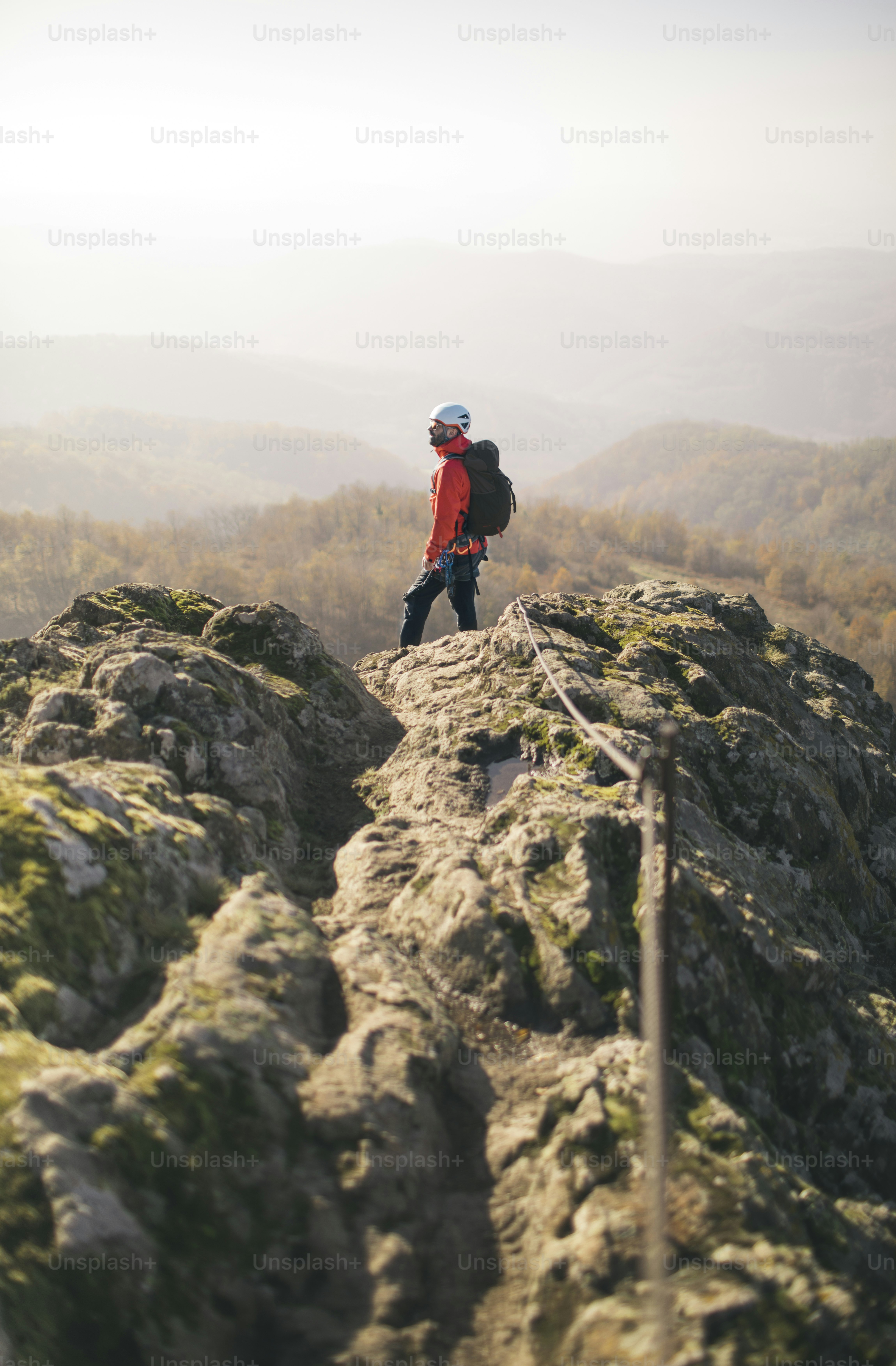 Mountaineer with backpack using climbing rope to climb rocky mountain ...