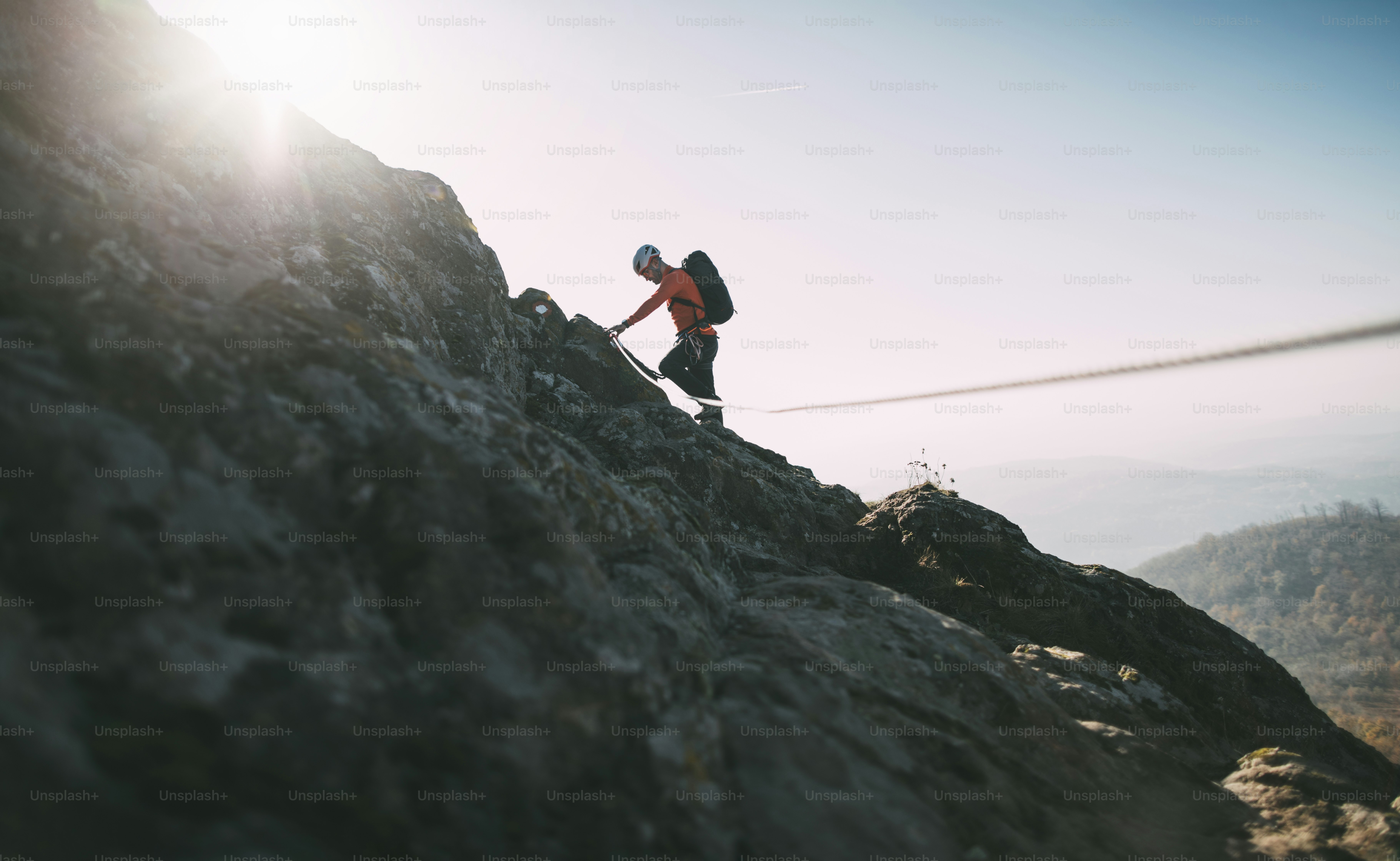 Mountaineer with backpack using climbing rope to climb rocky mountain ...