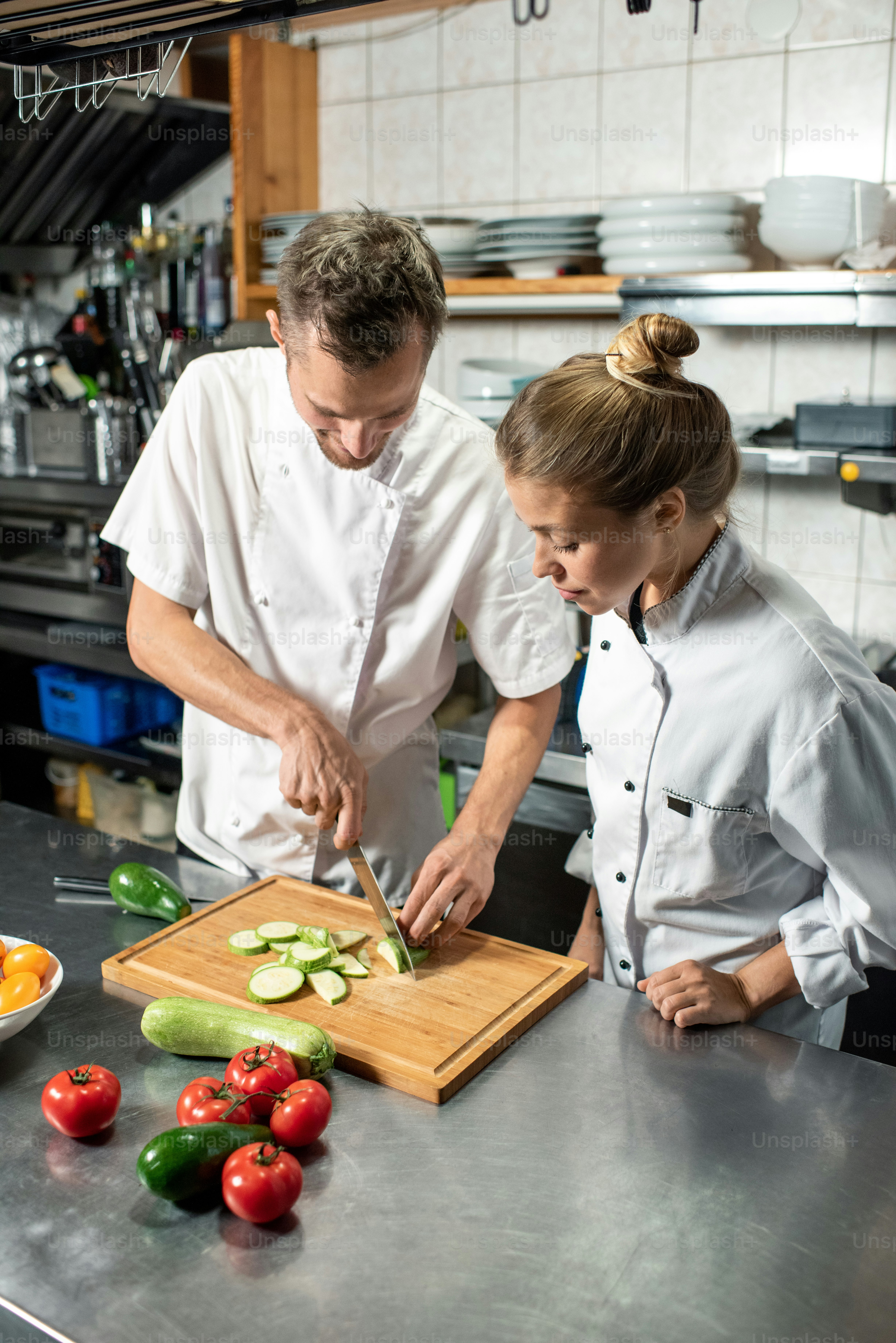 Young professional male chef showing his female trainee how to cook ...