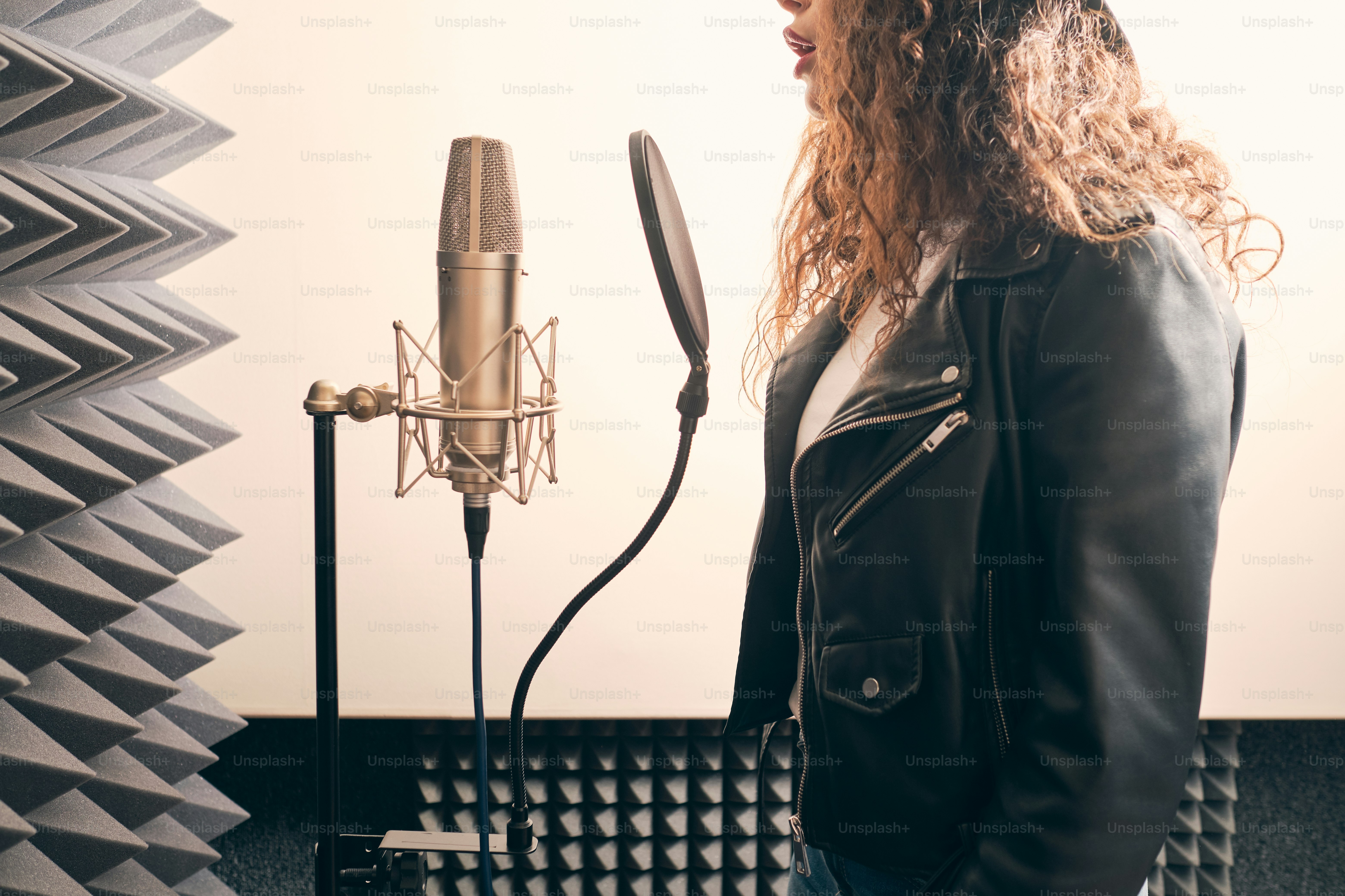 Portrait of beautiful curly woman in leather jacket recording vocals in ...