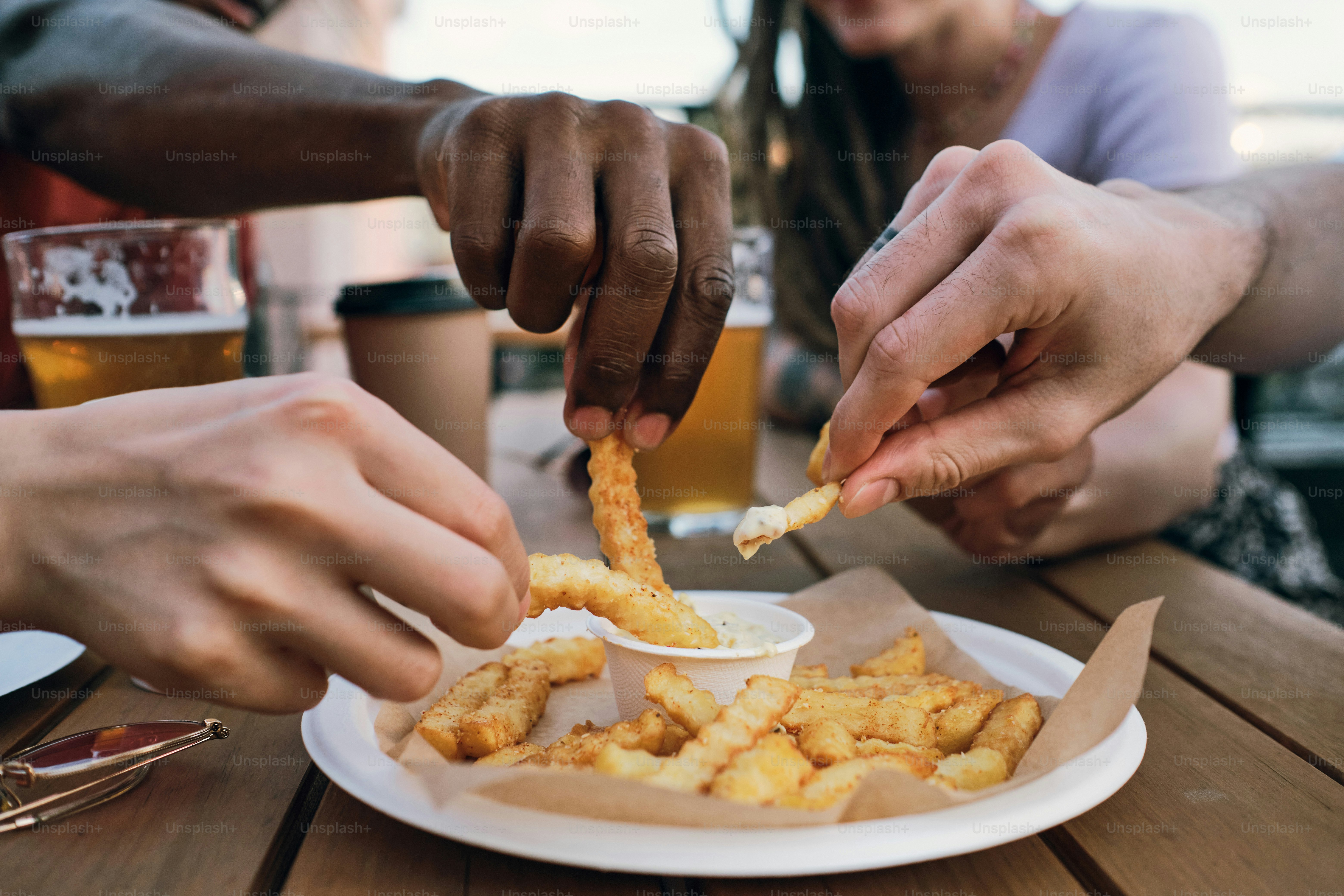 Hands of intercultural hungry friends putting french fries into sauce ...