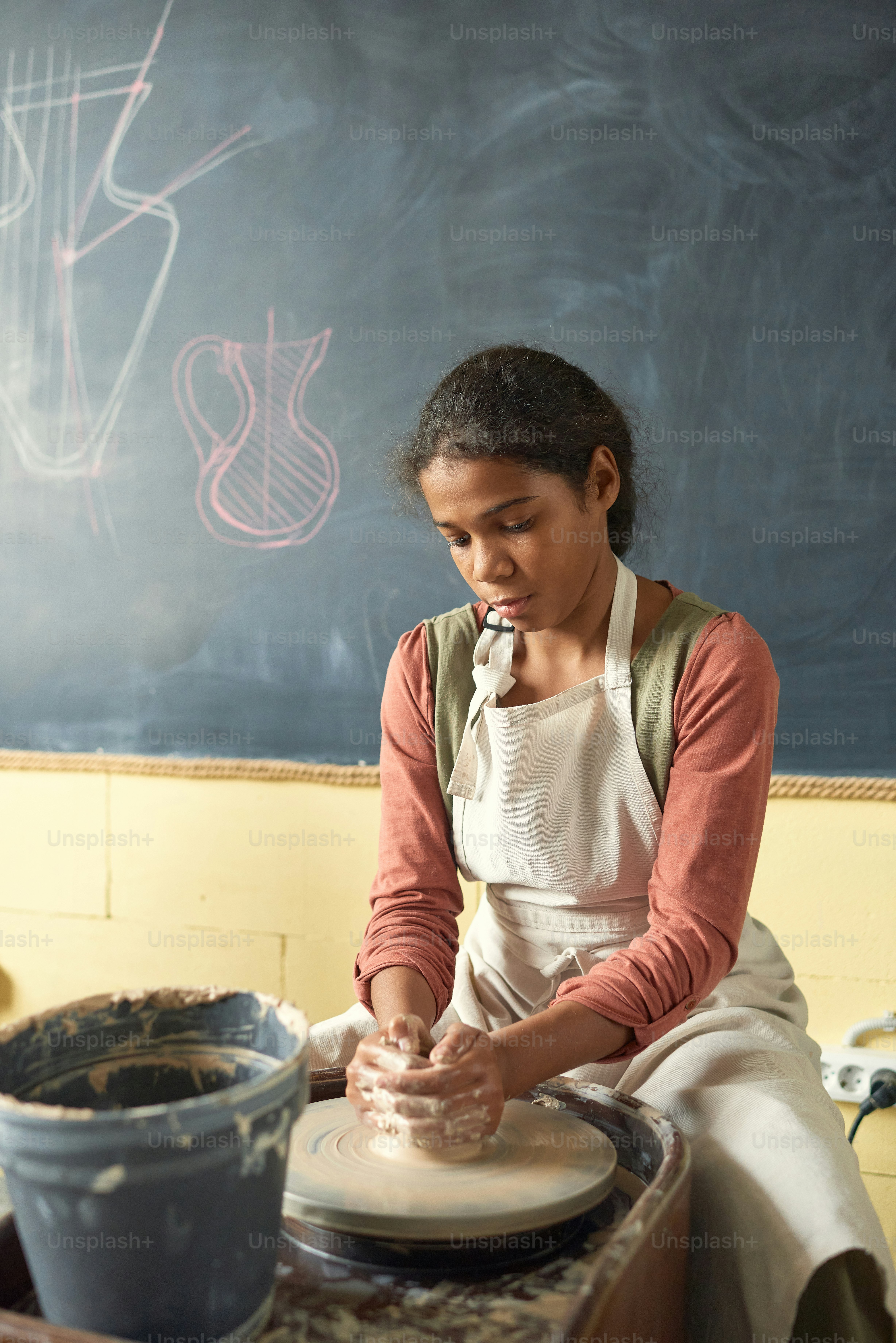 Jolie écolière africaine en tablier assis en tournant la roue de potier ...