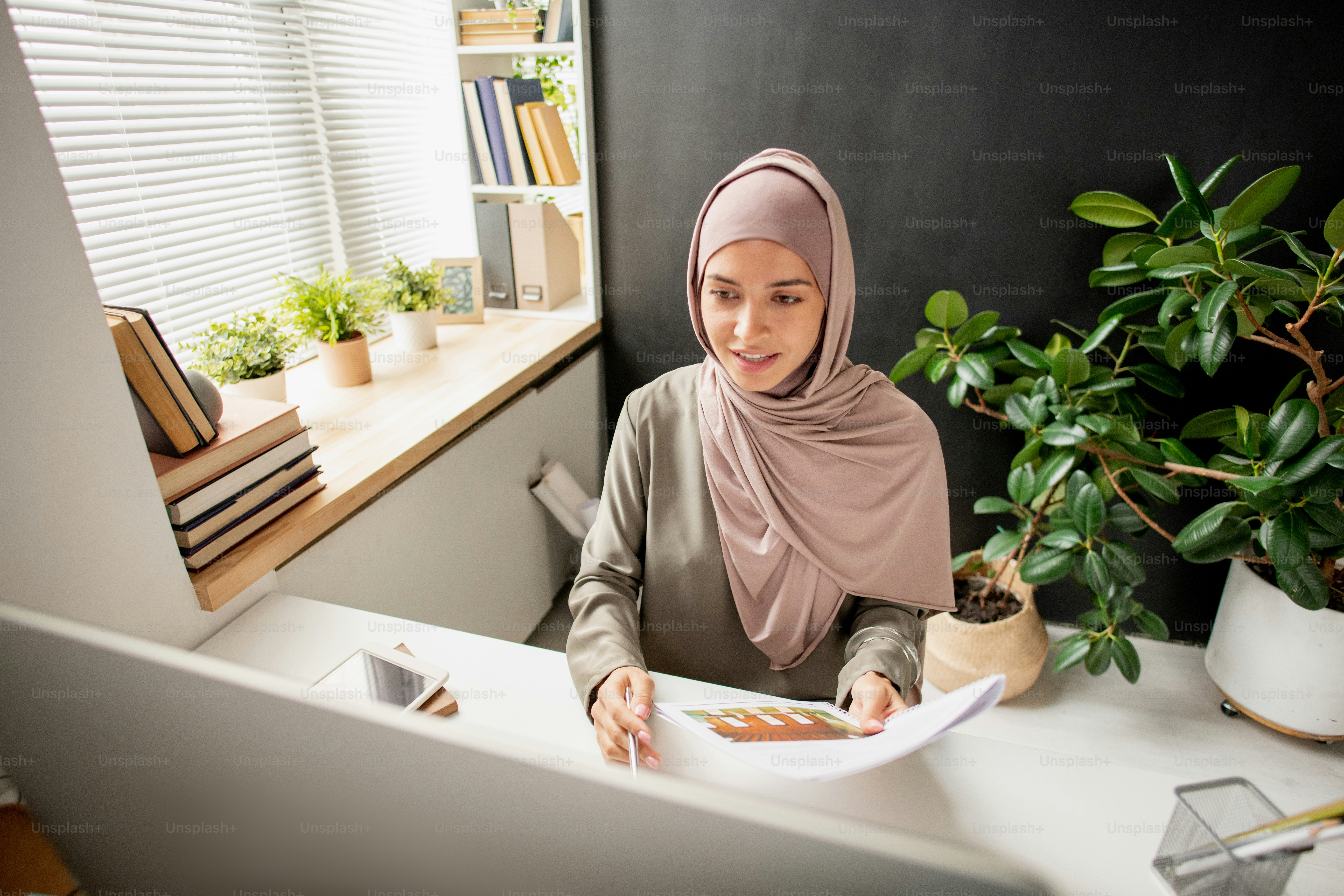 Successful young teacher in hijab looking at computer screen during ...