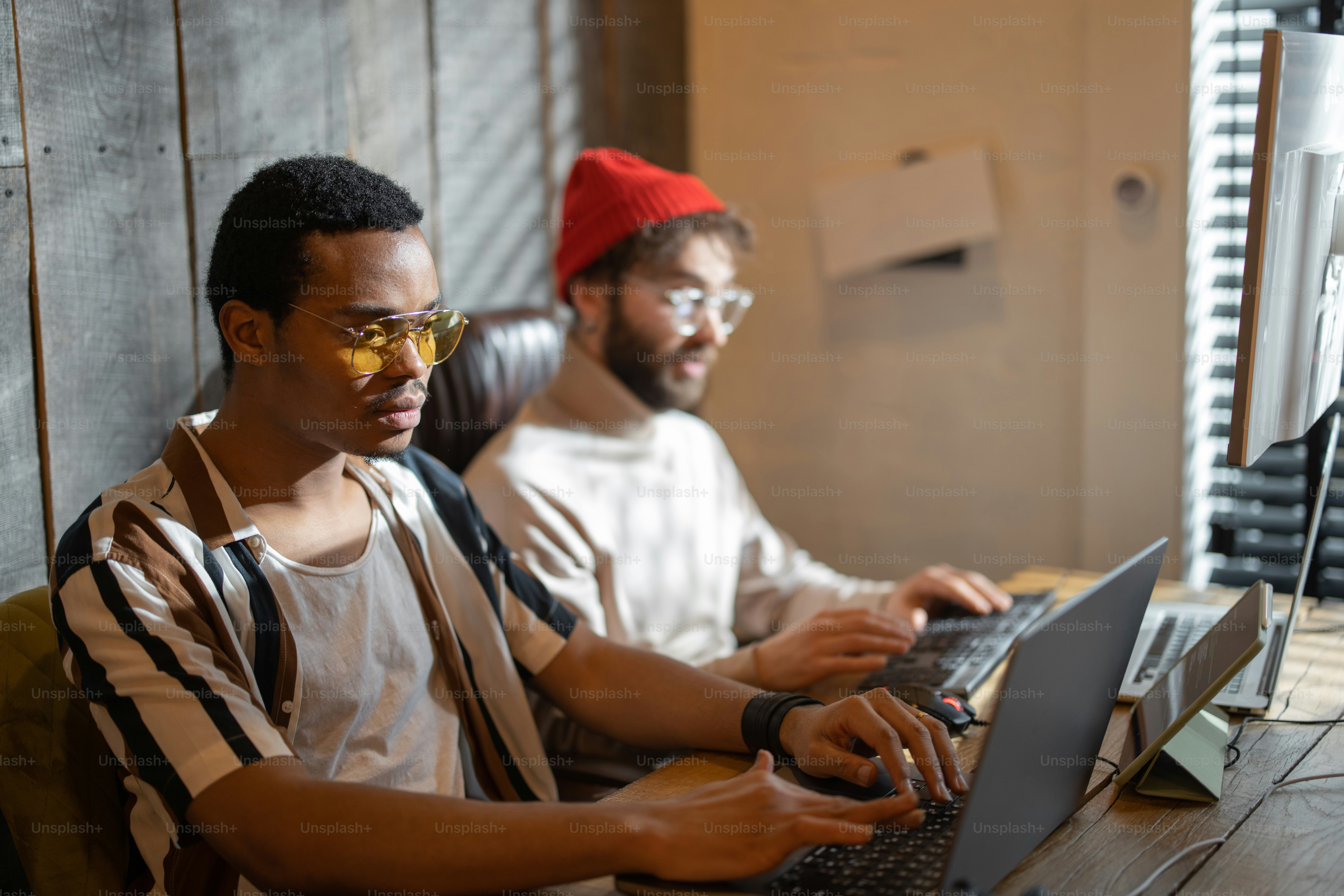 Two men with different nationality working on computers, sitting ...