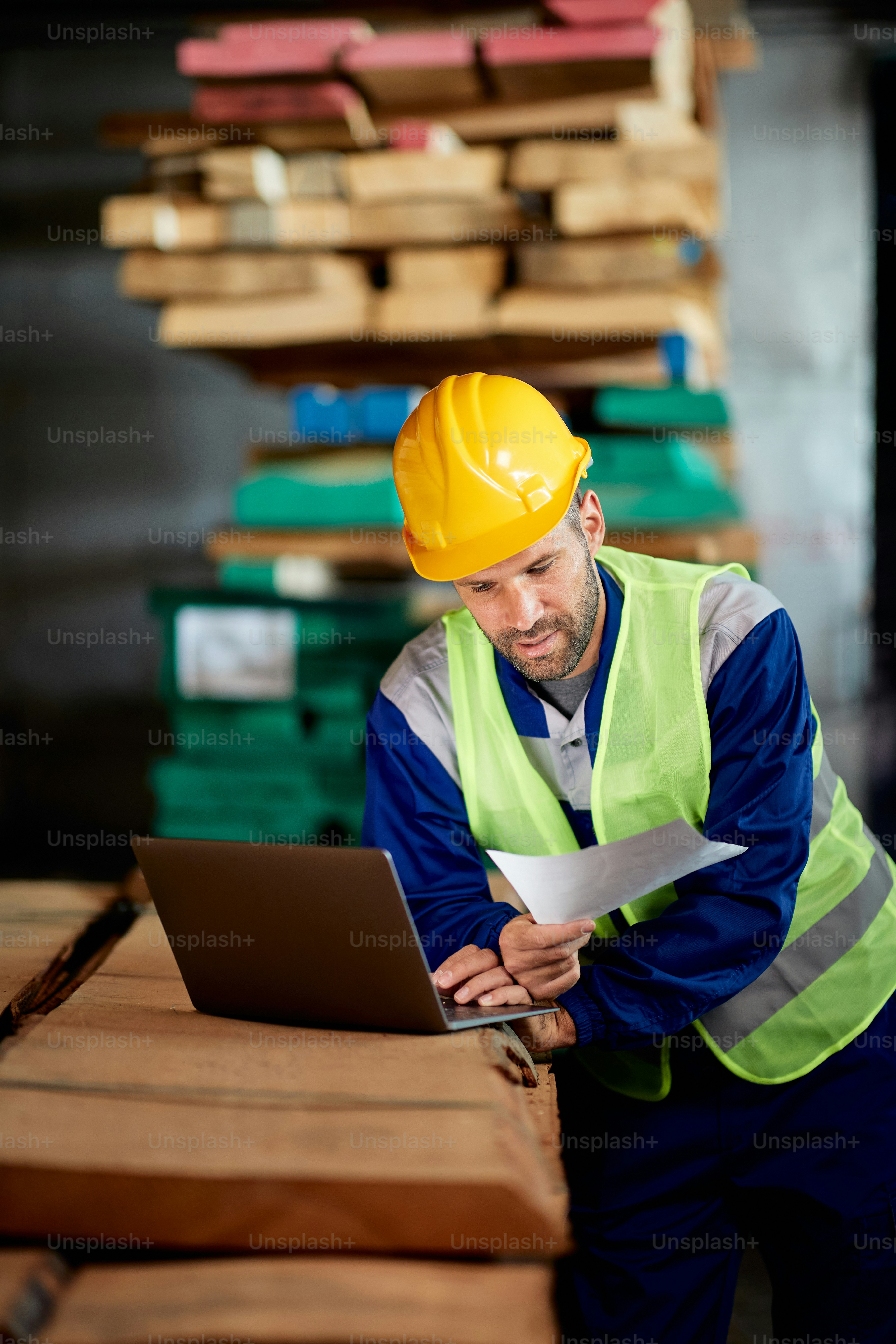 Wood warehouse worker using laptop while going through paperwork at ...