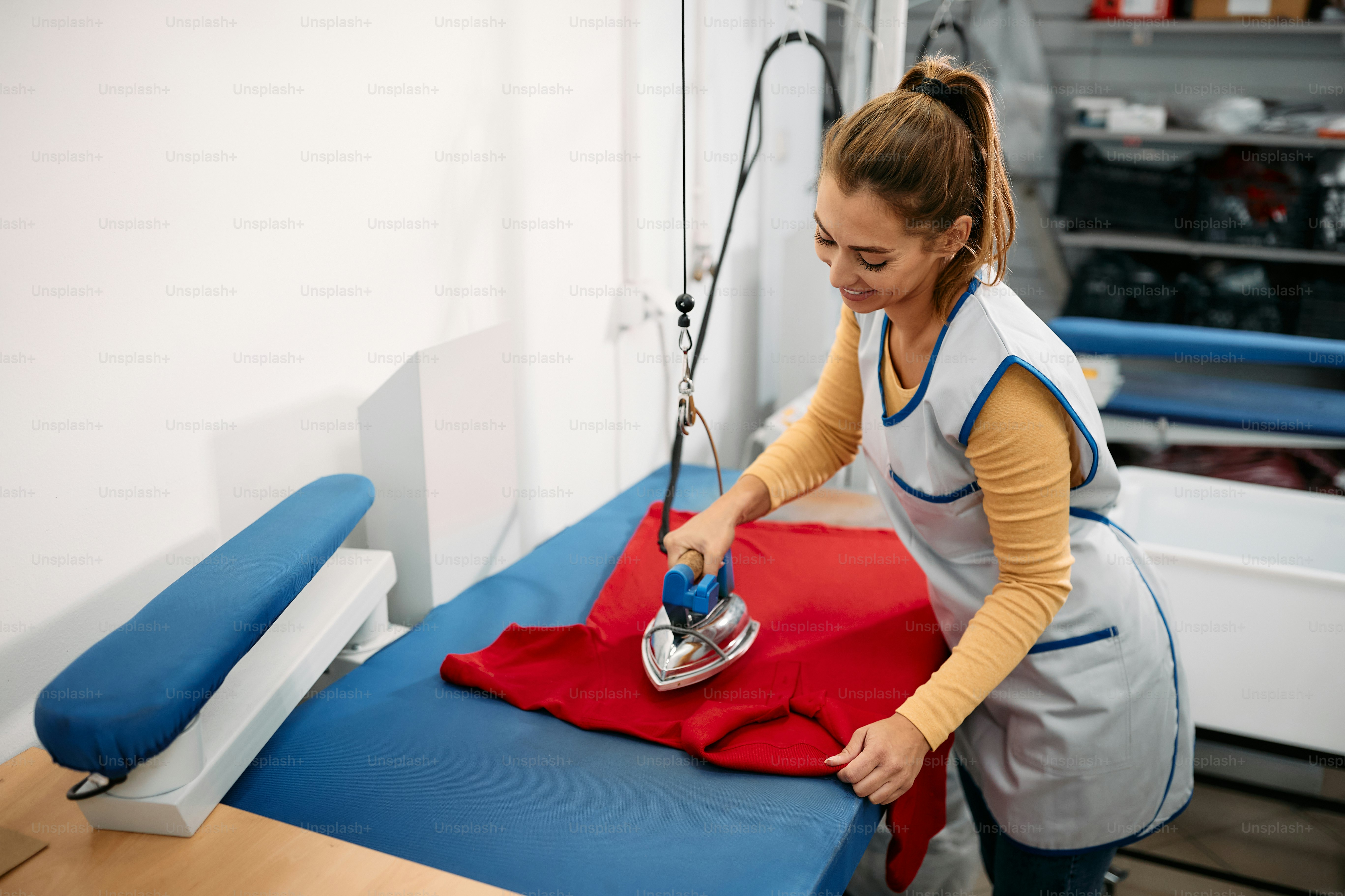 Young happy woman ironing clothing while working at textile factory ...