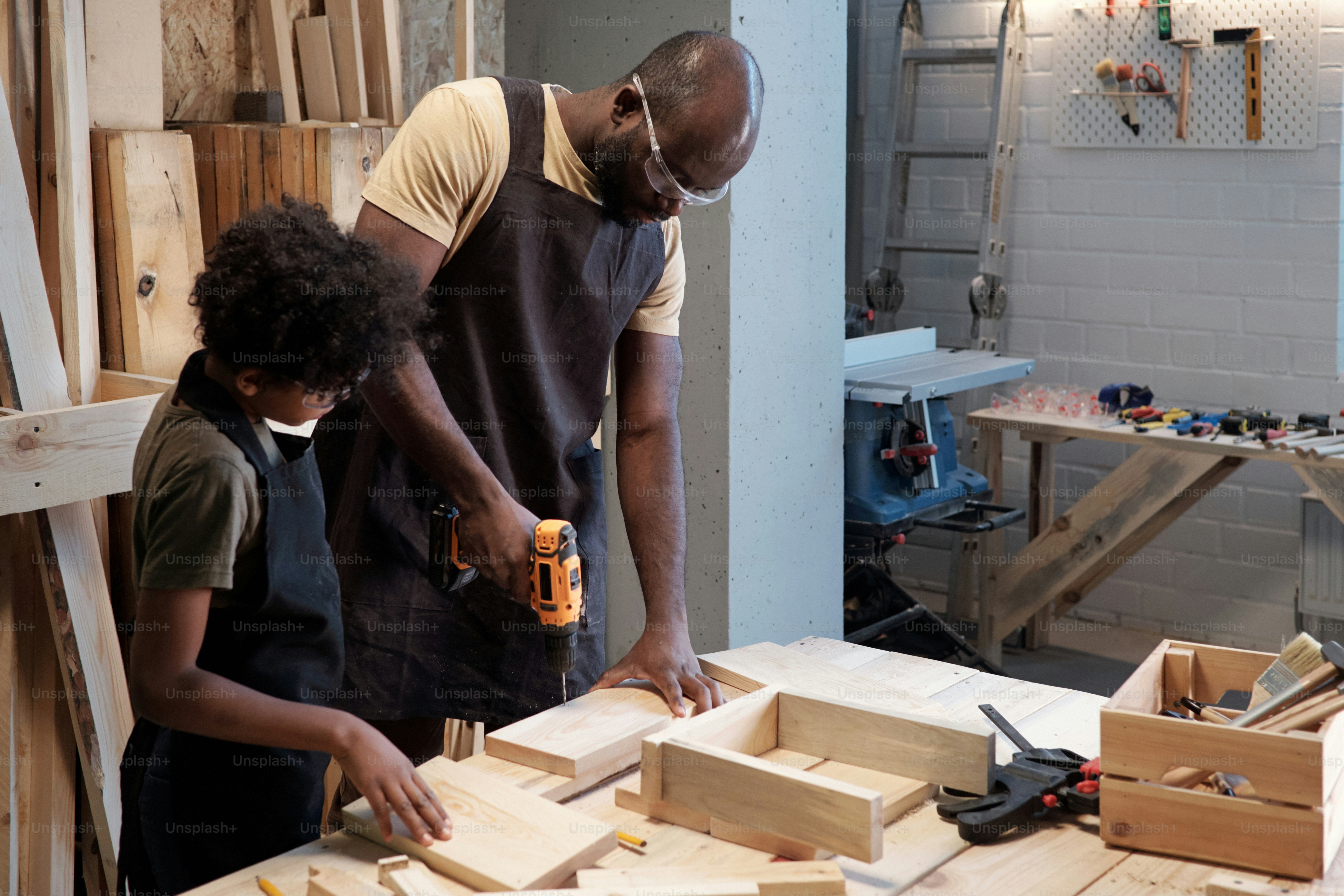 Portrait of African-American father and son building birdhouse together in garage workshop photo ...