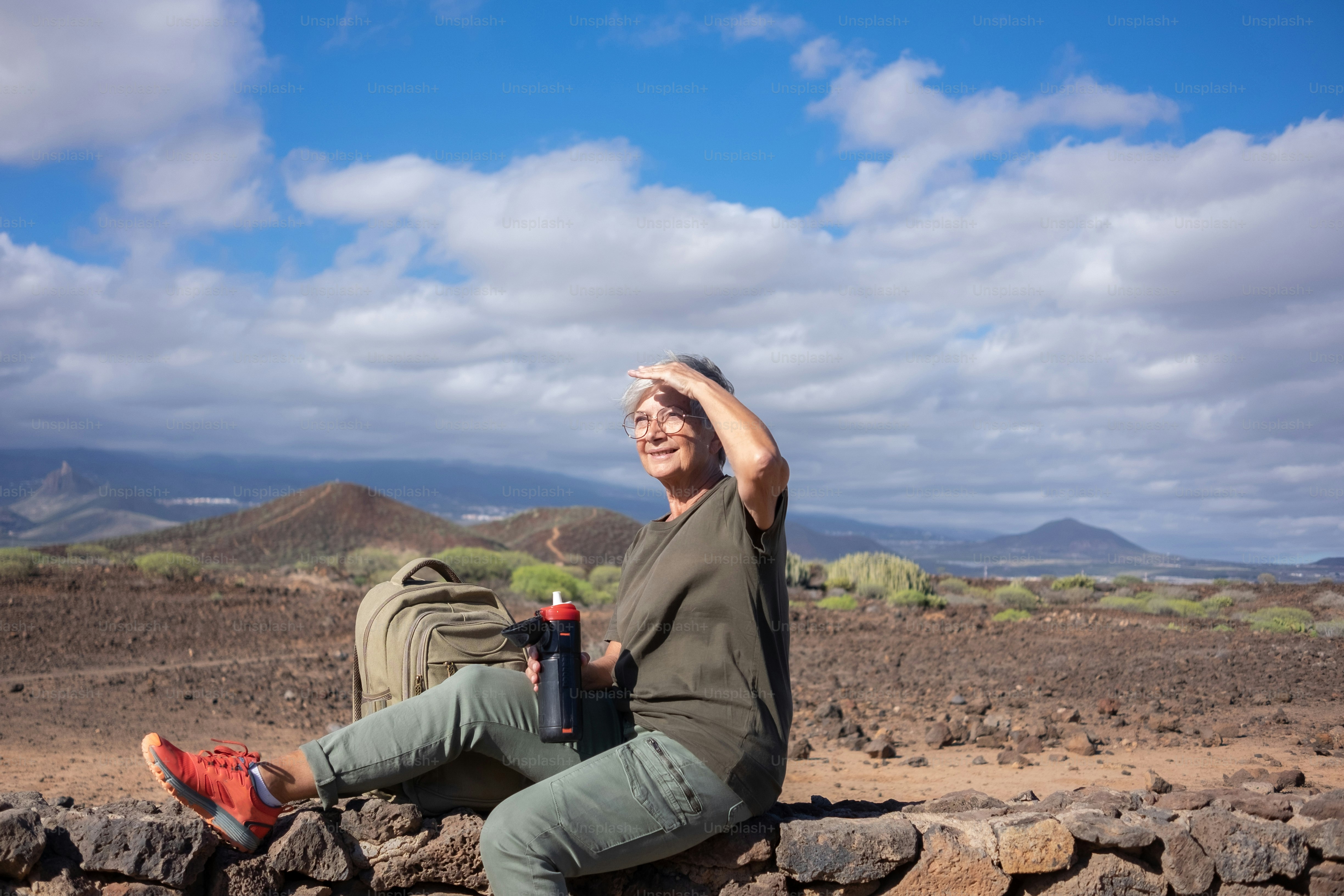 Smiling elderly woman on outdoor hike sitting on a stone wall holding ...