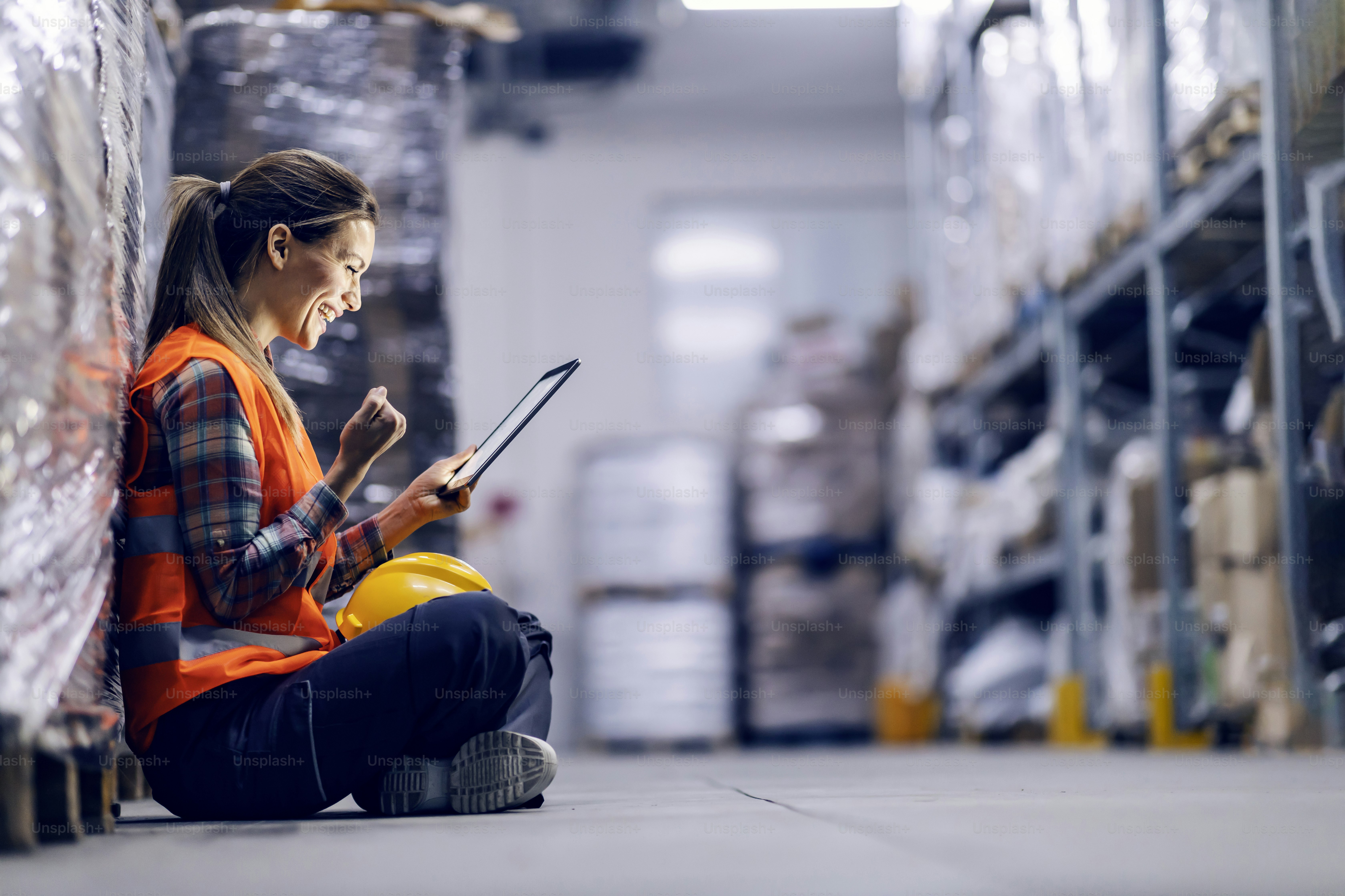 Happy female warehouse worker on the floor looking at touch pad and ...