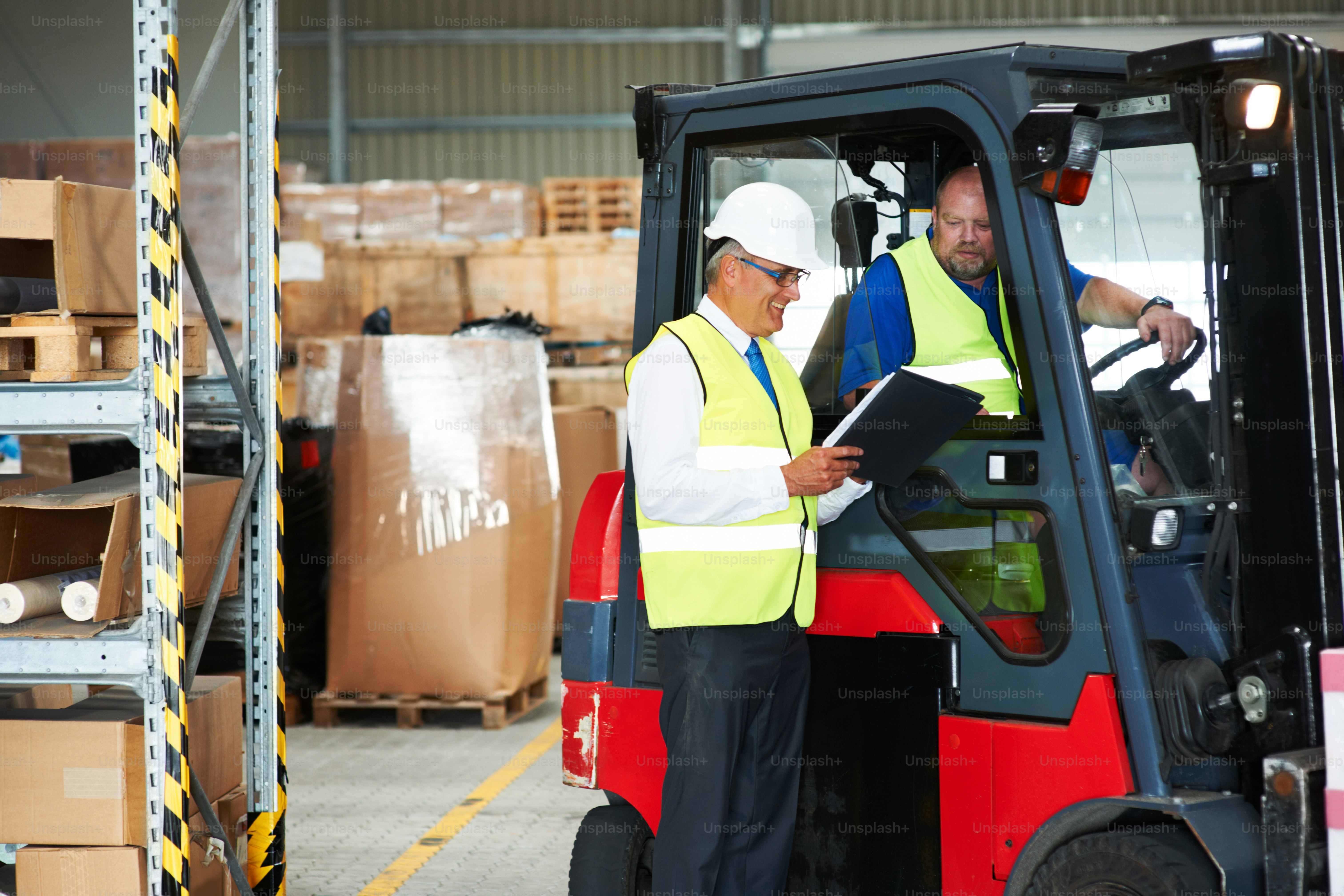 Two men in safety vests standing next to a forklift photo – Cheerful ...