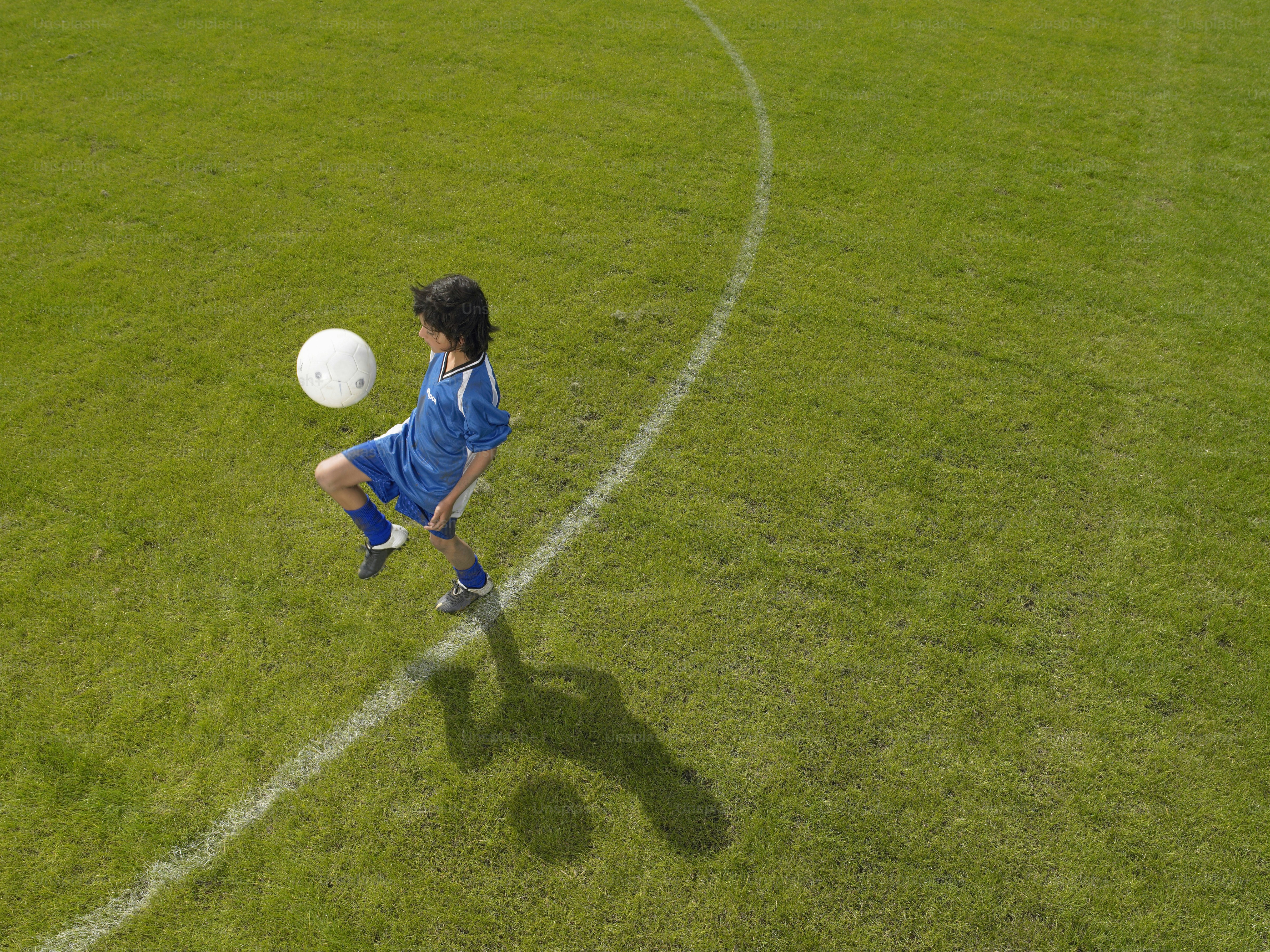 A young boy kicking a soccer ball across a field photo – Human shadow ...