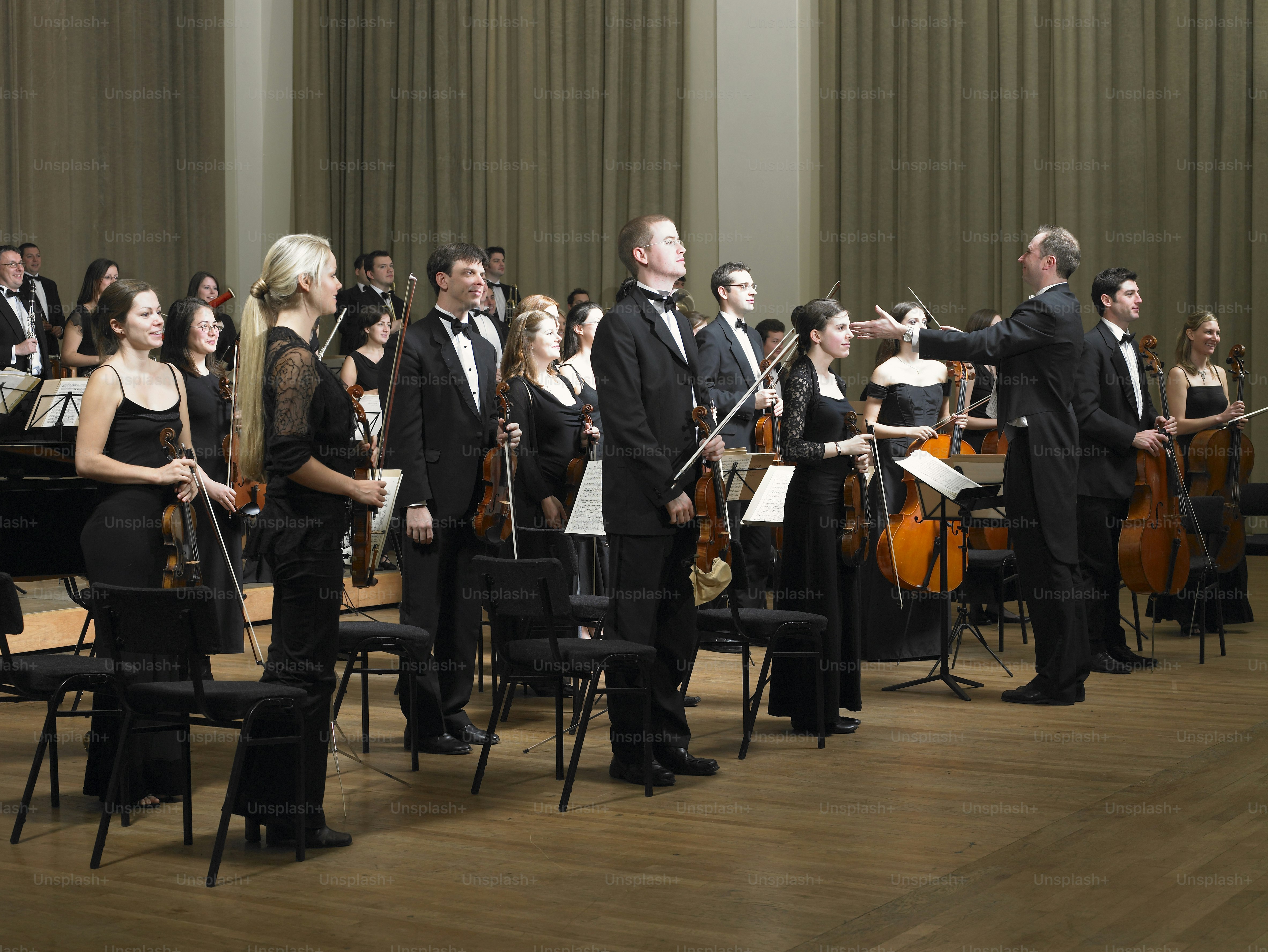 A conductor and orchestra in a large room photo – Orchestra Image on ...