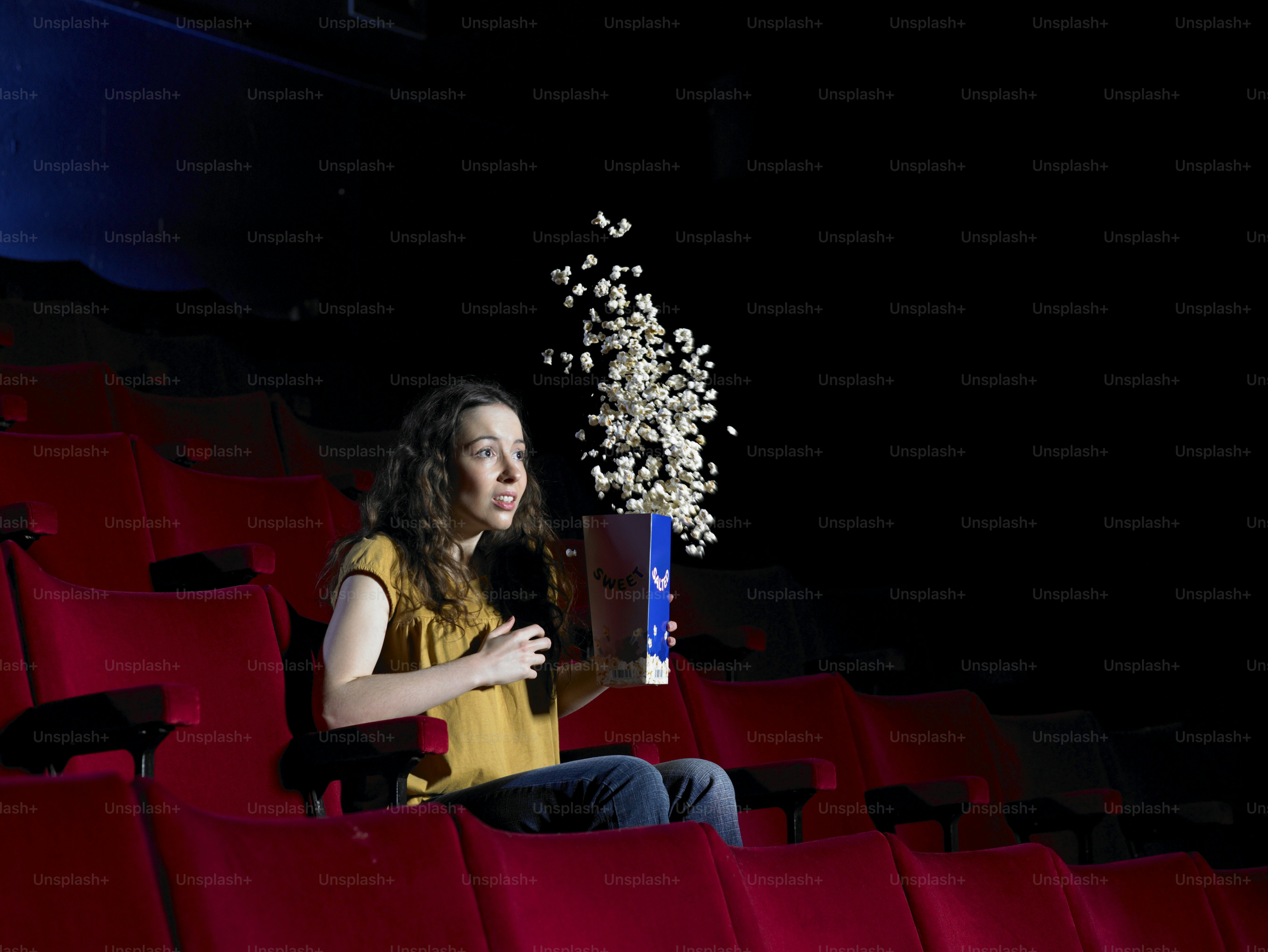 A woman sitting in a theater holding a box of popcorn photo – Suspense ...