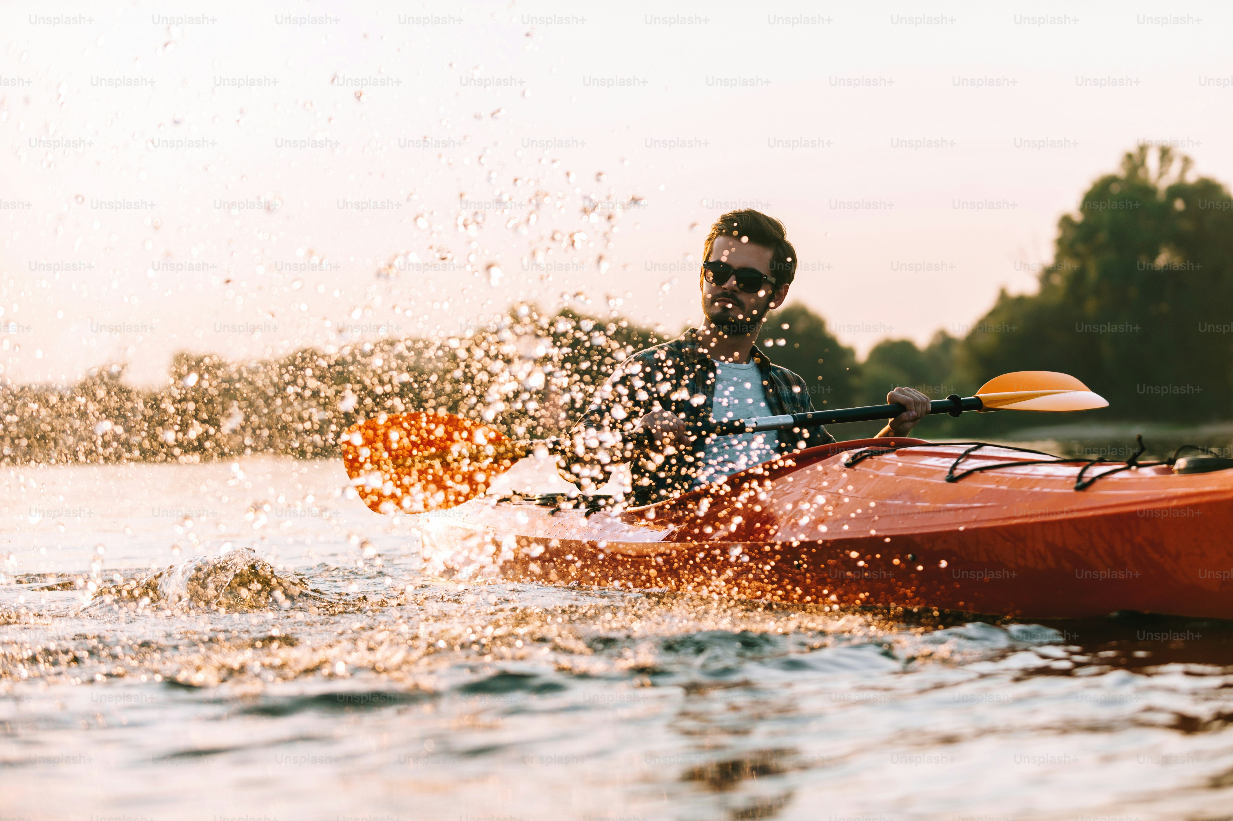 Handsome young man kayaking on lake with sunset in the background photo ...
