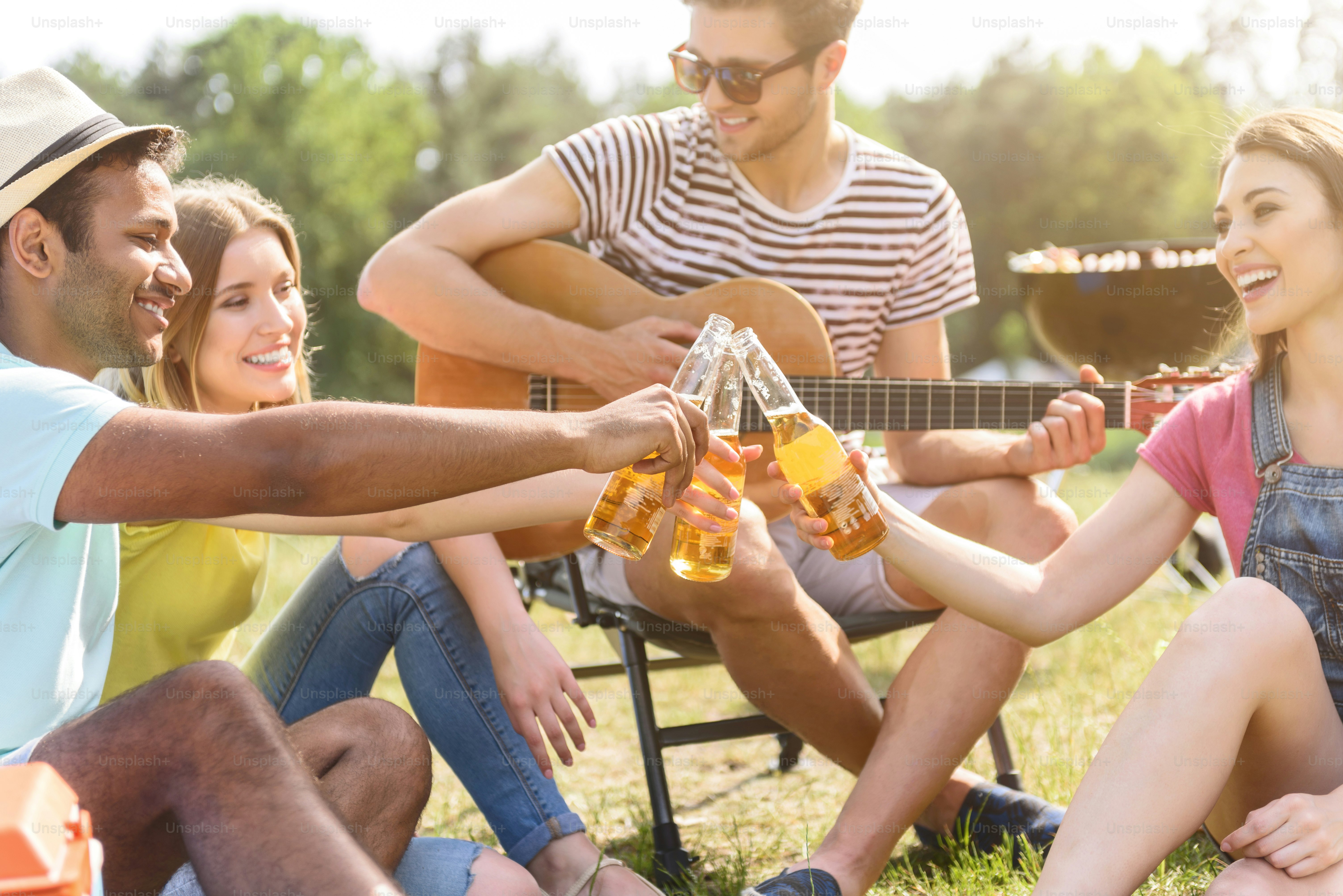 Young people having rest in nature together. They are drinking beer and ...