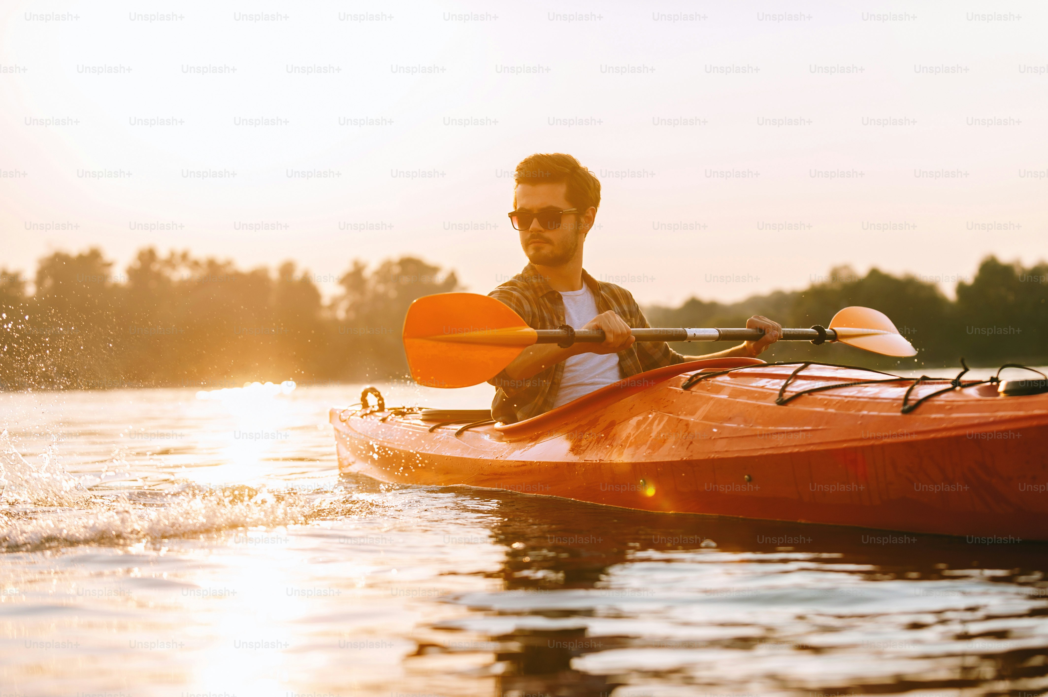 Handsome young man kayaking on lake with sunset in the background photo ...