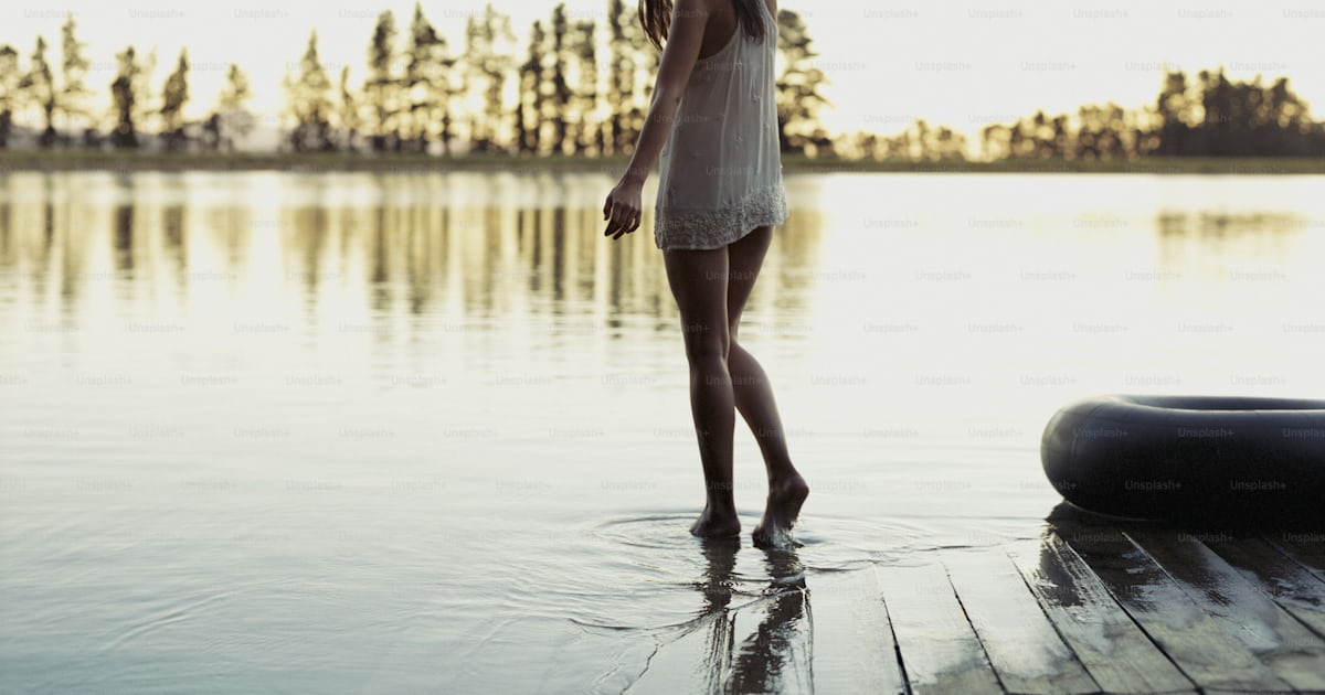 Foto zum Thema Eine Frau, die auf einem Dock neben einem Gewässer steht ... Foto zum Thema Eine Frau, die auf einem Dock neben einem Gewässer steht ...