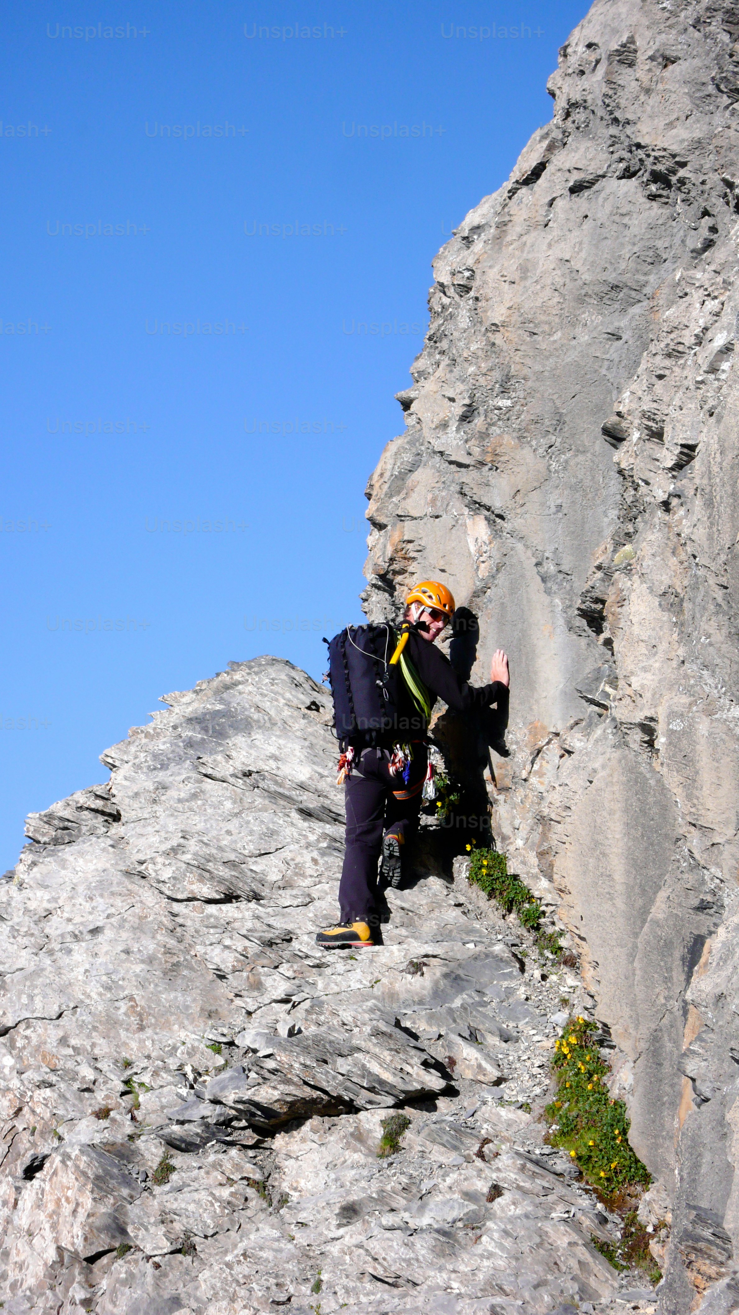 A male mountain climber at the start of a long climbing route under a ...