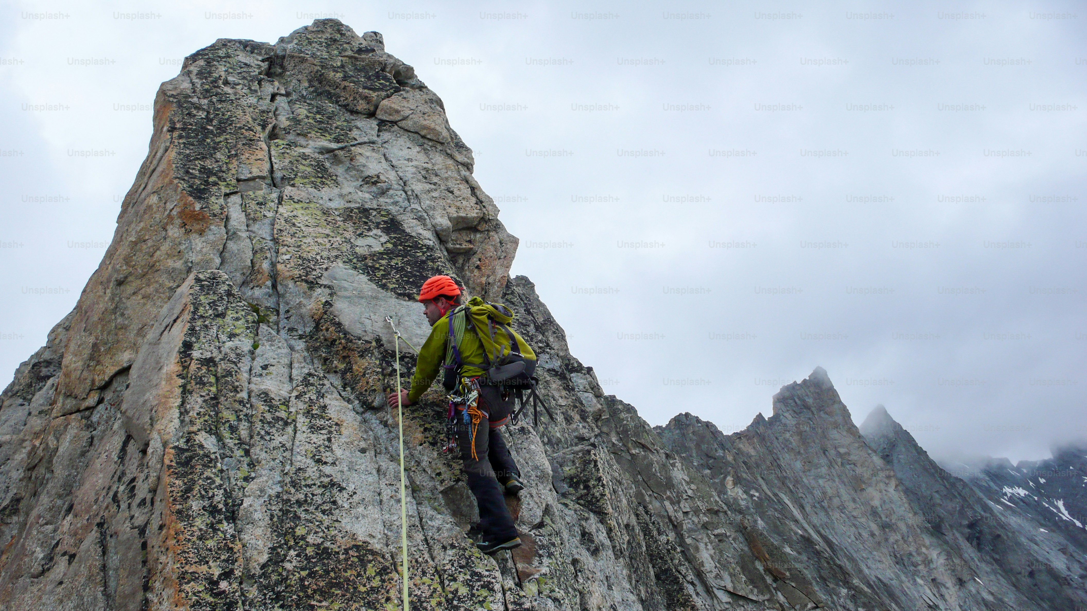 A male mountain guide lead climbing on an exposed granite ridge in the ...